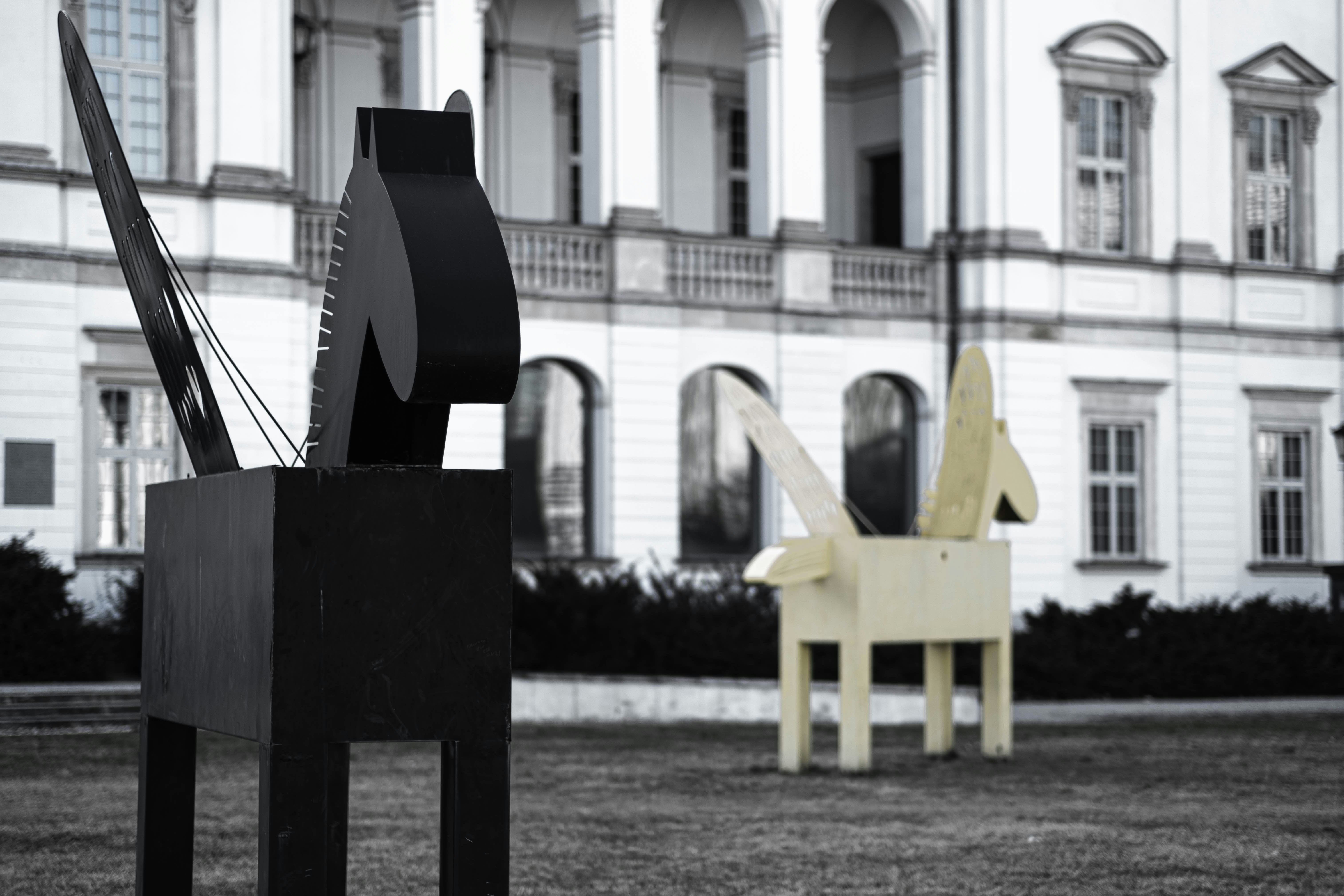 Two large animal sculptures, one black and one yellow, stand in front of a classic architectural backdrop, creating a striking visual contrast.