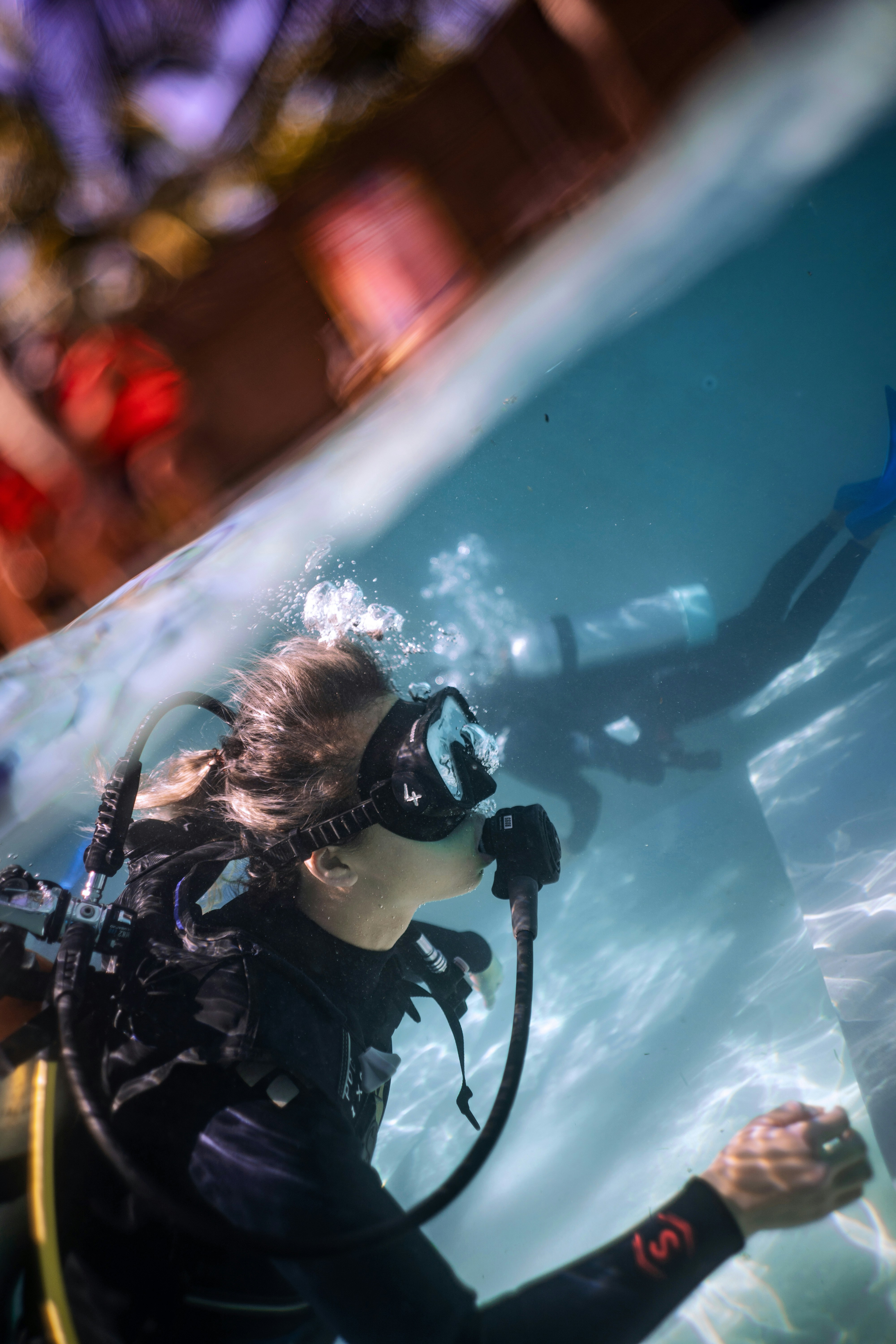 Diver in scuba gear submerged in a swimming pool with sunlight creating dynamic reflections.