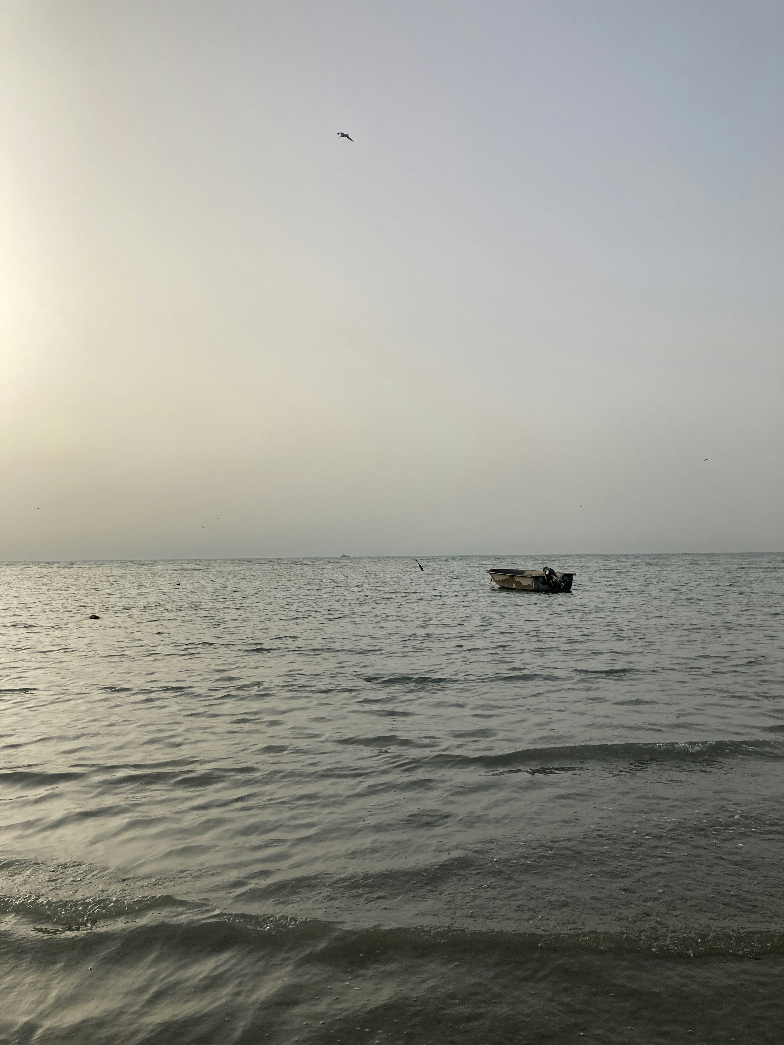 A solitary fishing boat glides across a tranquil sea under a soft, hazy sky, evoking a sense of calm and solitude.