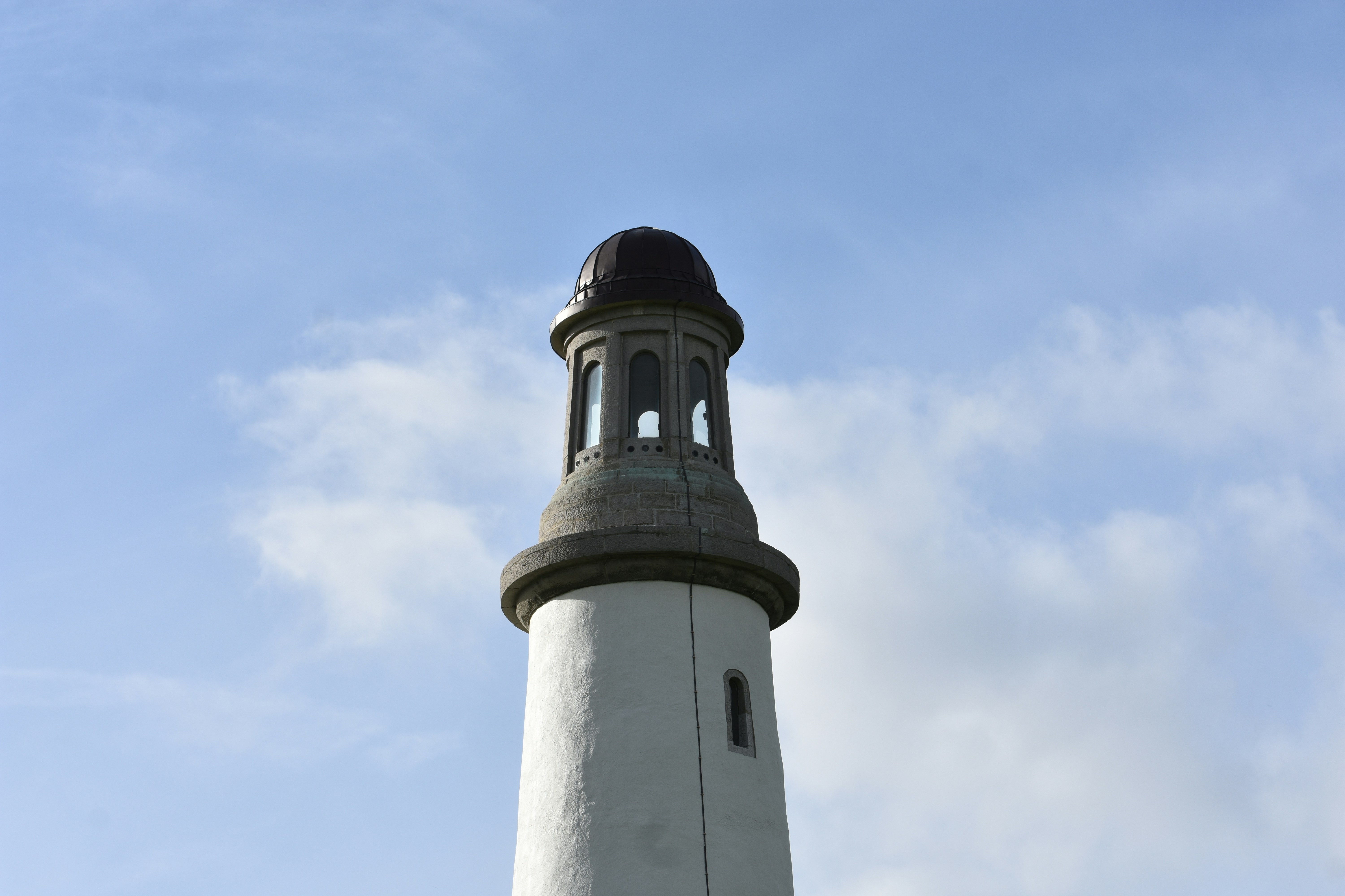 A historic lighthouse stands tall against a clear blue sky, showcasing its unique architectural features and weathered charm.