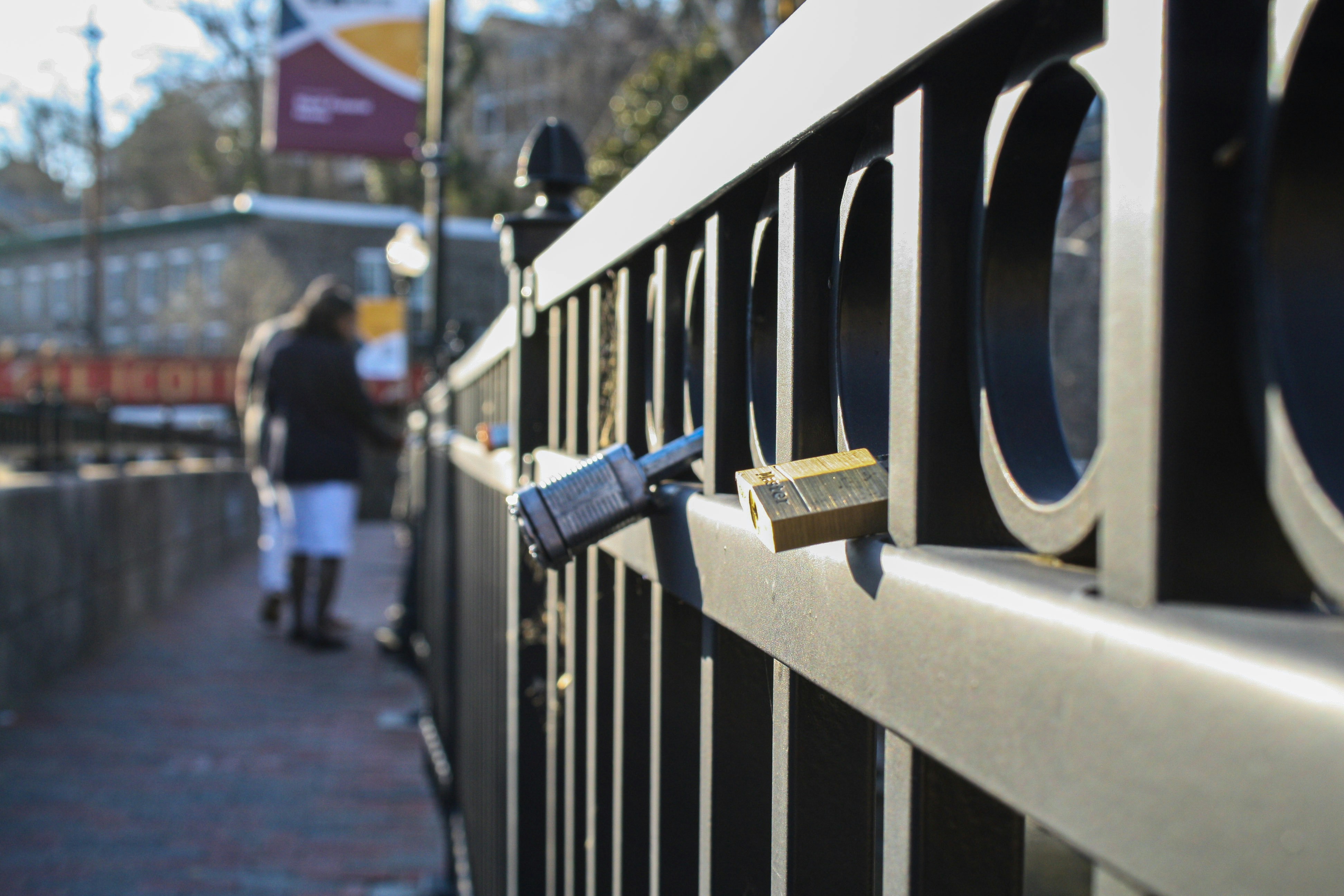 a couple of people walking down a sidewalk next to a fence