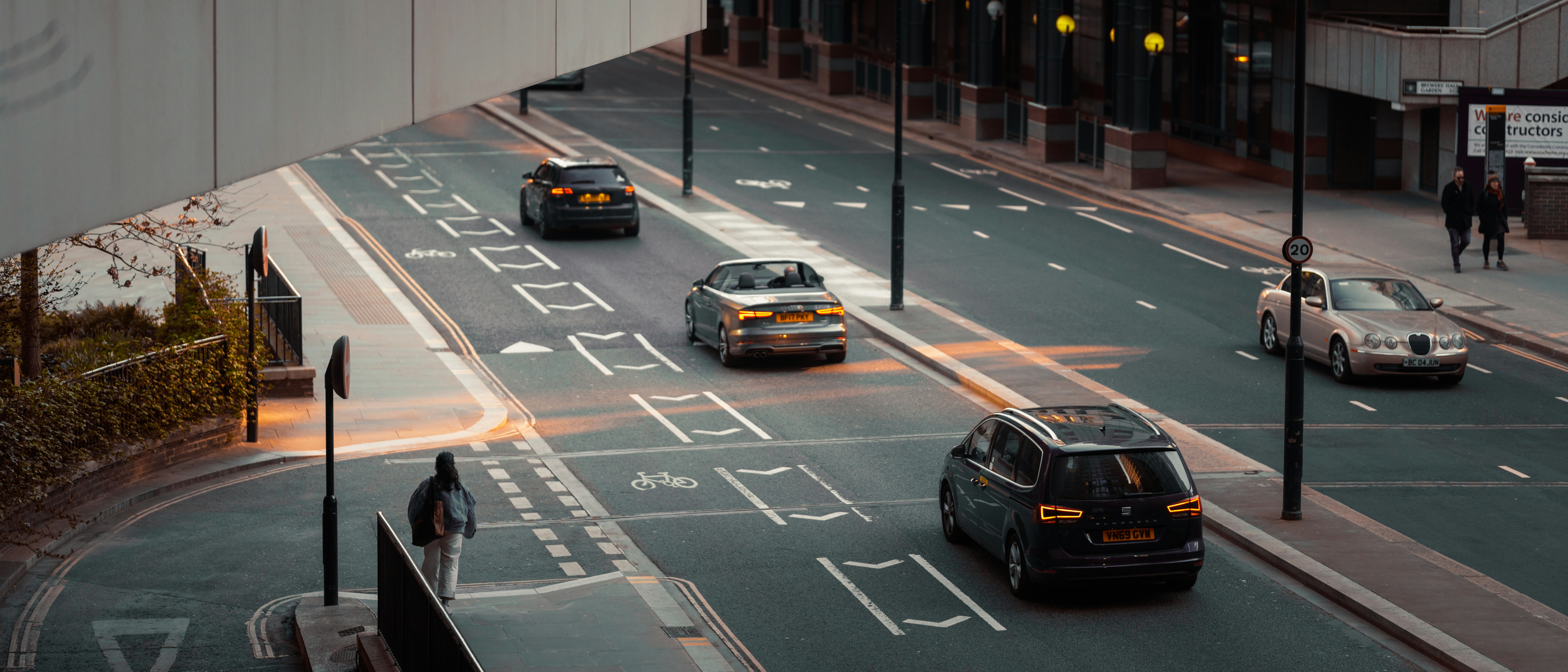 A bustling city street scene featuring cars navigating through a modern urban landscape, illuminated by warm streetlights in the evening.