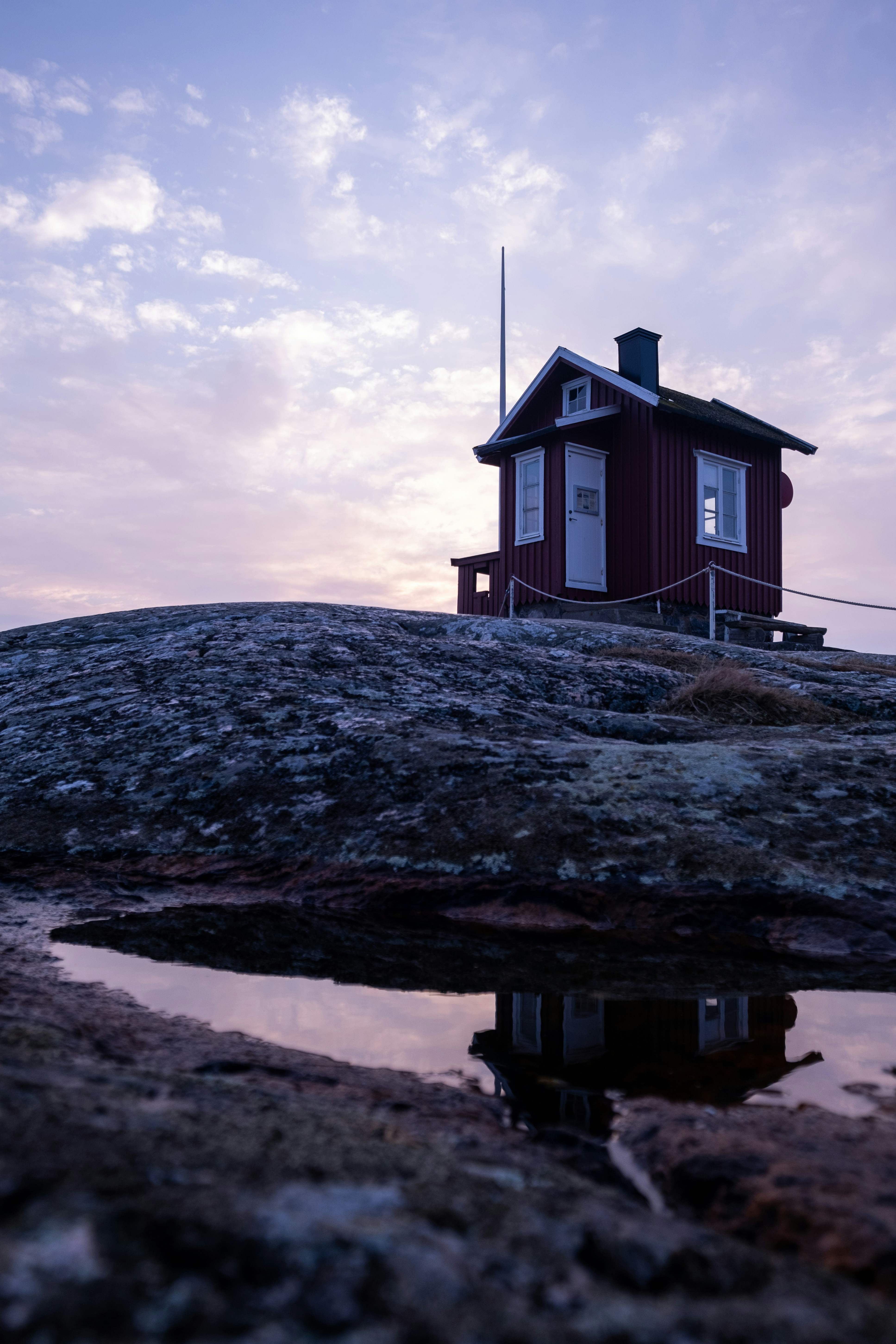 A Lone Red Cabin Crowned on the Rocky Promontory at Dusk