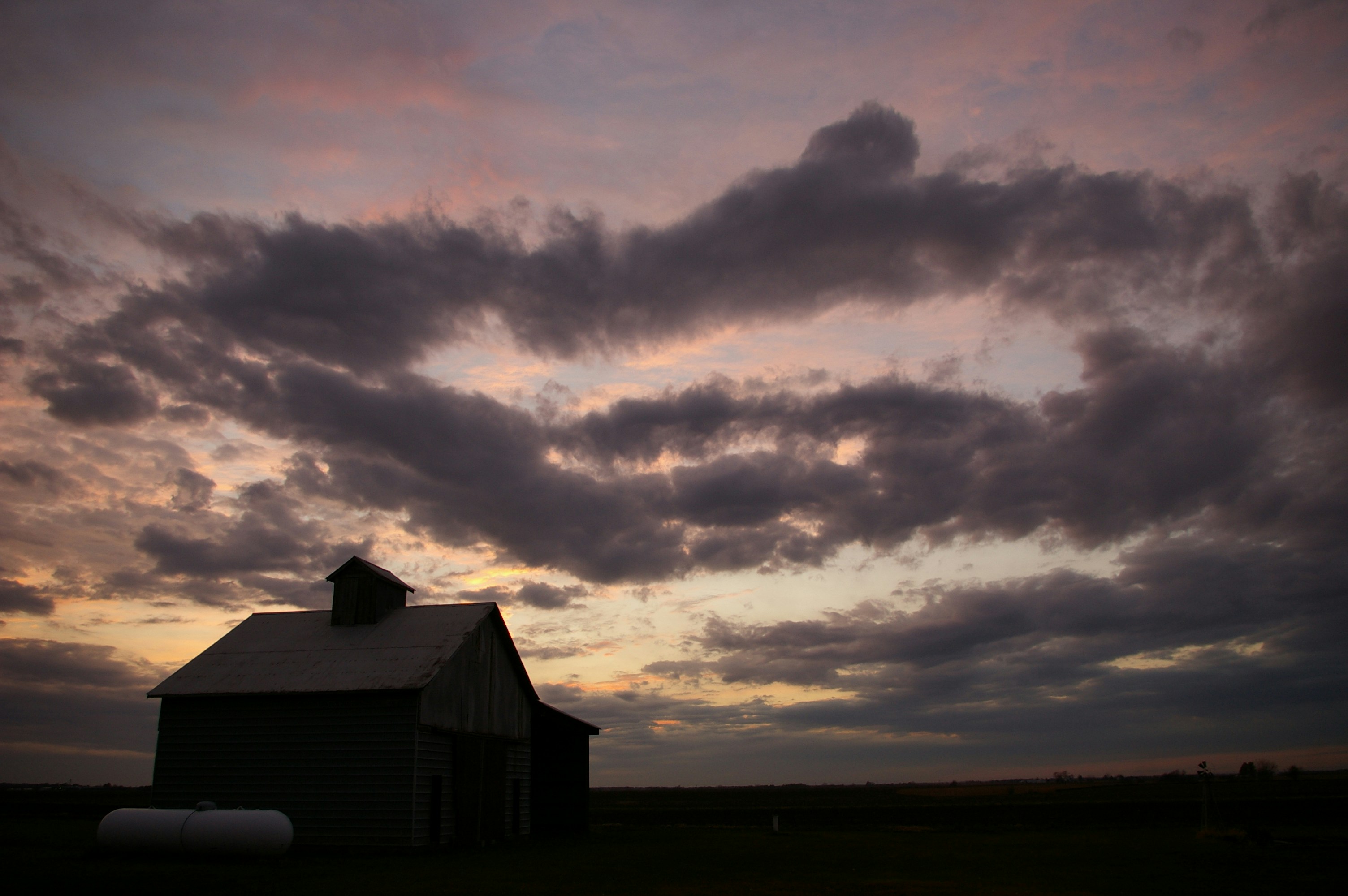 Silhouetted barn against a dramatic sky filled with swirling clouds at twilight.