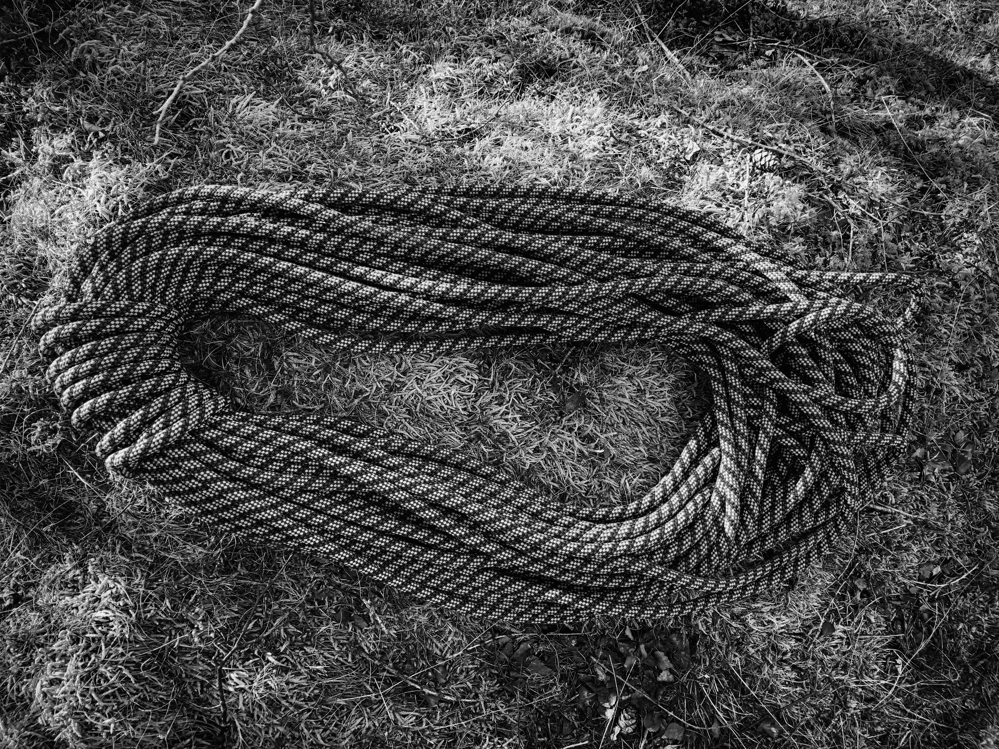 A coiled rope resting on a textured surface, showcasing intricate patterns and shadows. The monochrome presentation emphasizes the form and details of the rope.