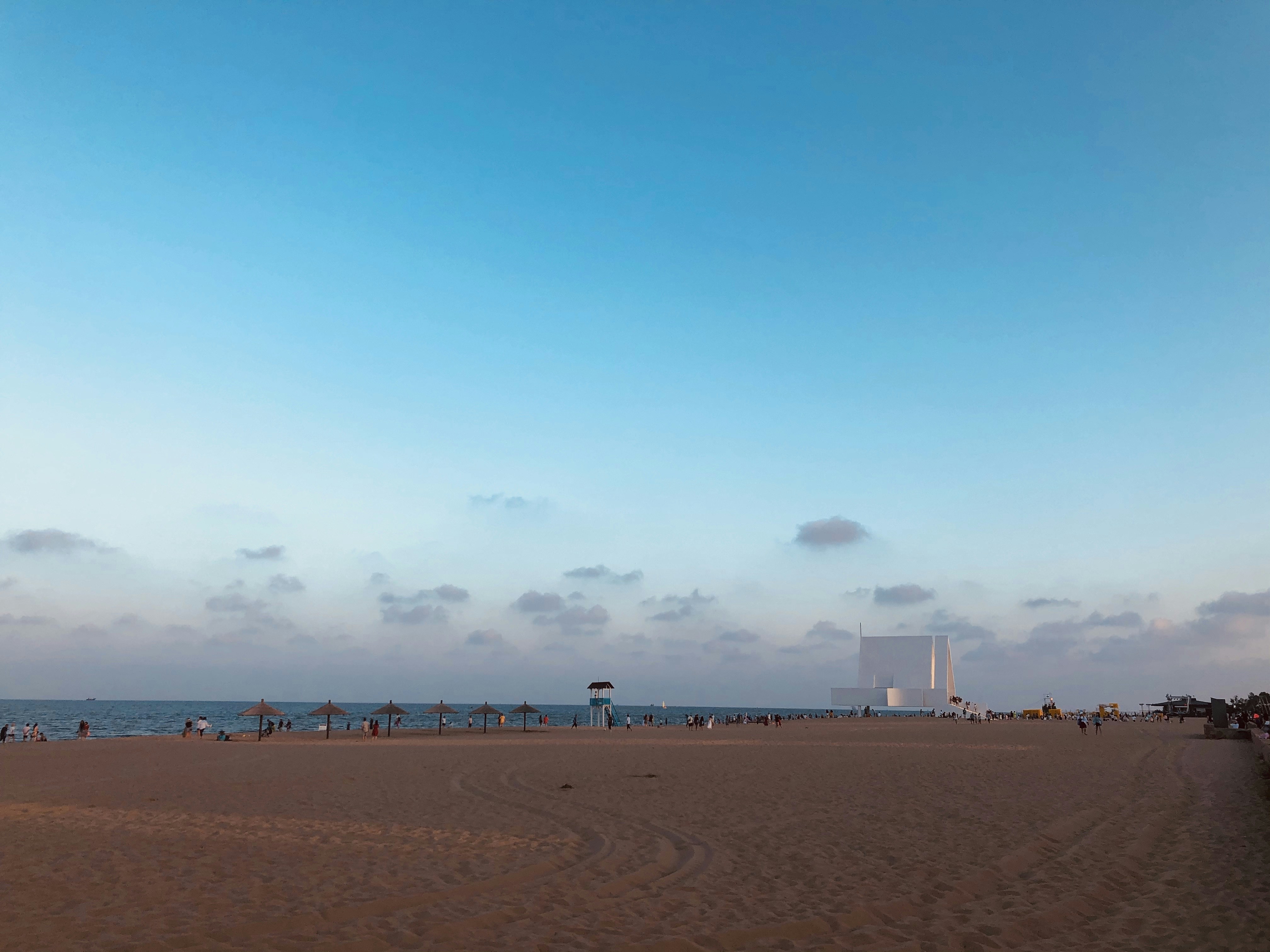 Sandy beach stretching to a distant horizon under a blue sky with scattered clouds.