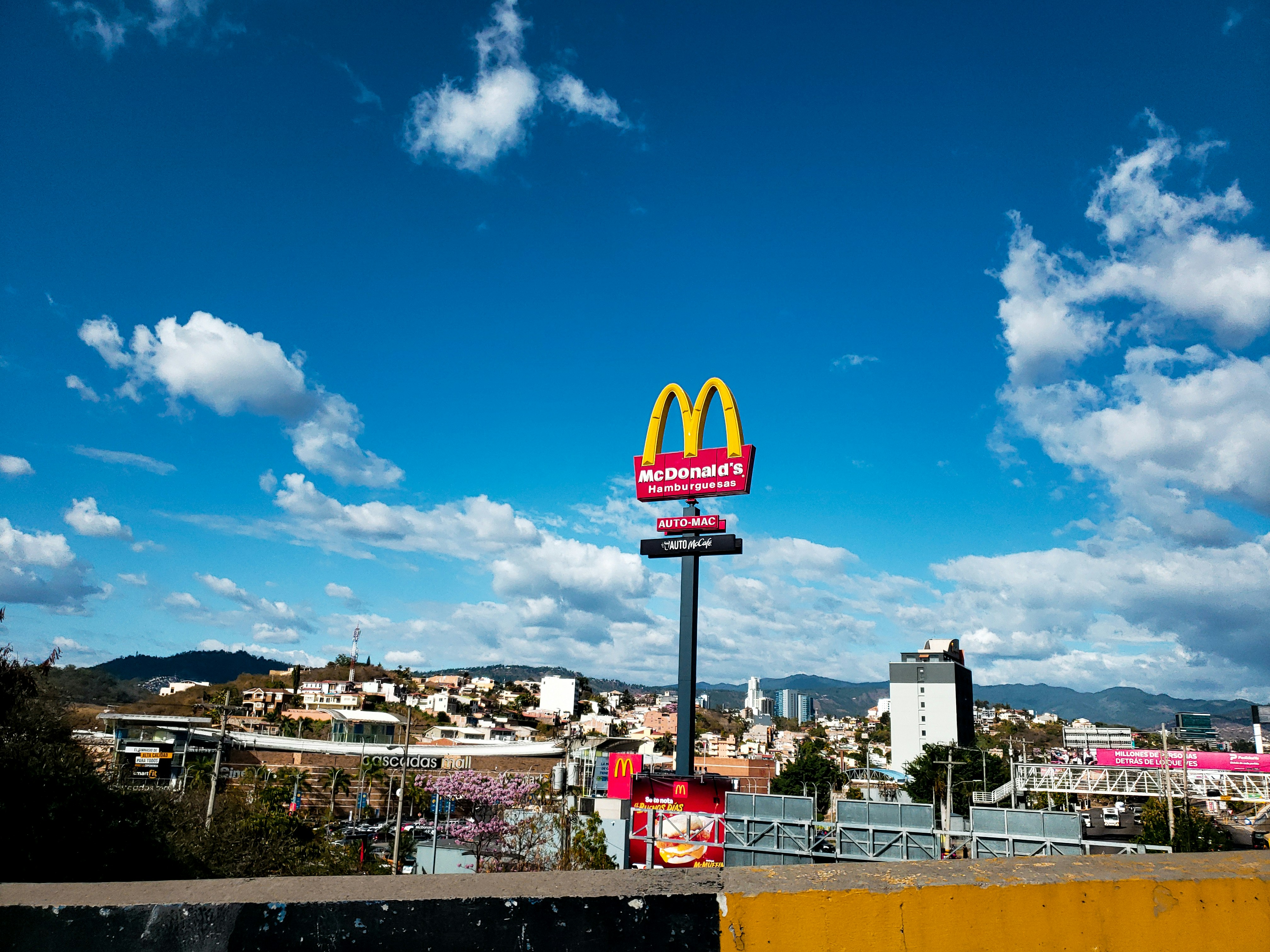 McDonald's sign stands tall against a vivid blue sky with scattered clouds.