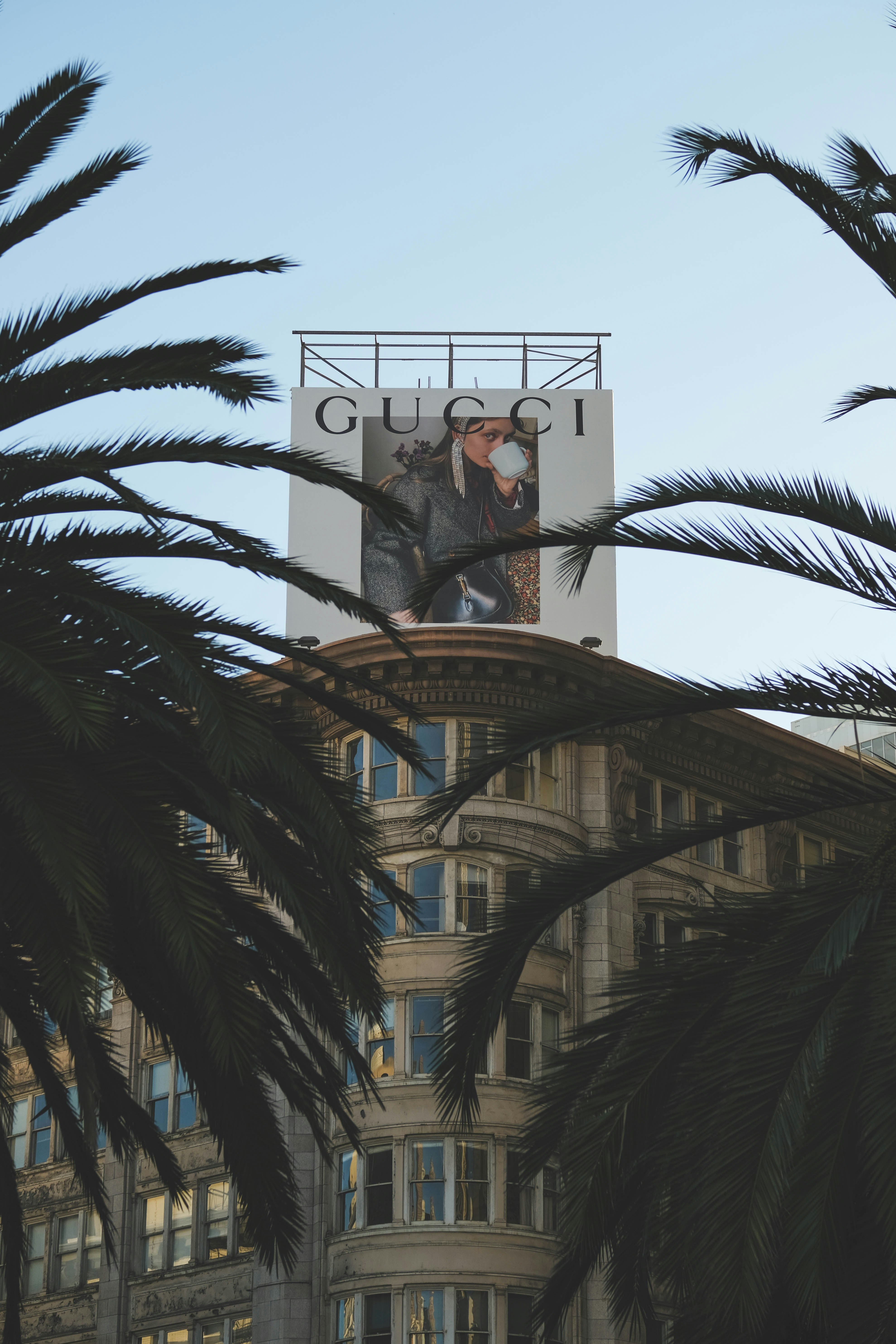 Gucci Banner Framed by Swaying Palms Over a Classic City Facade