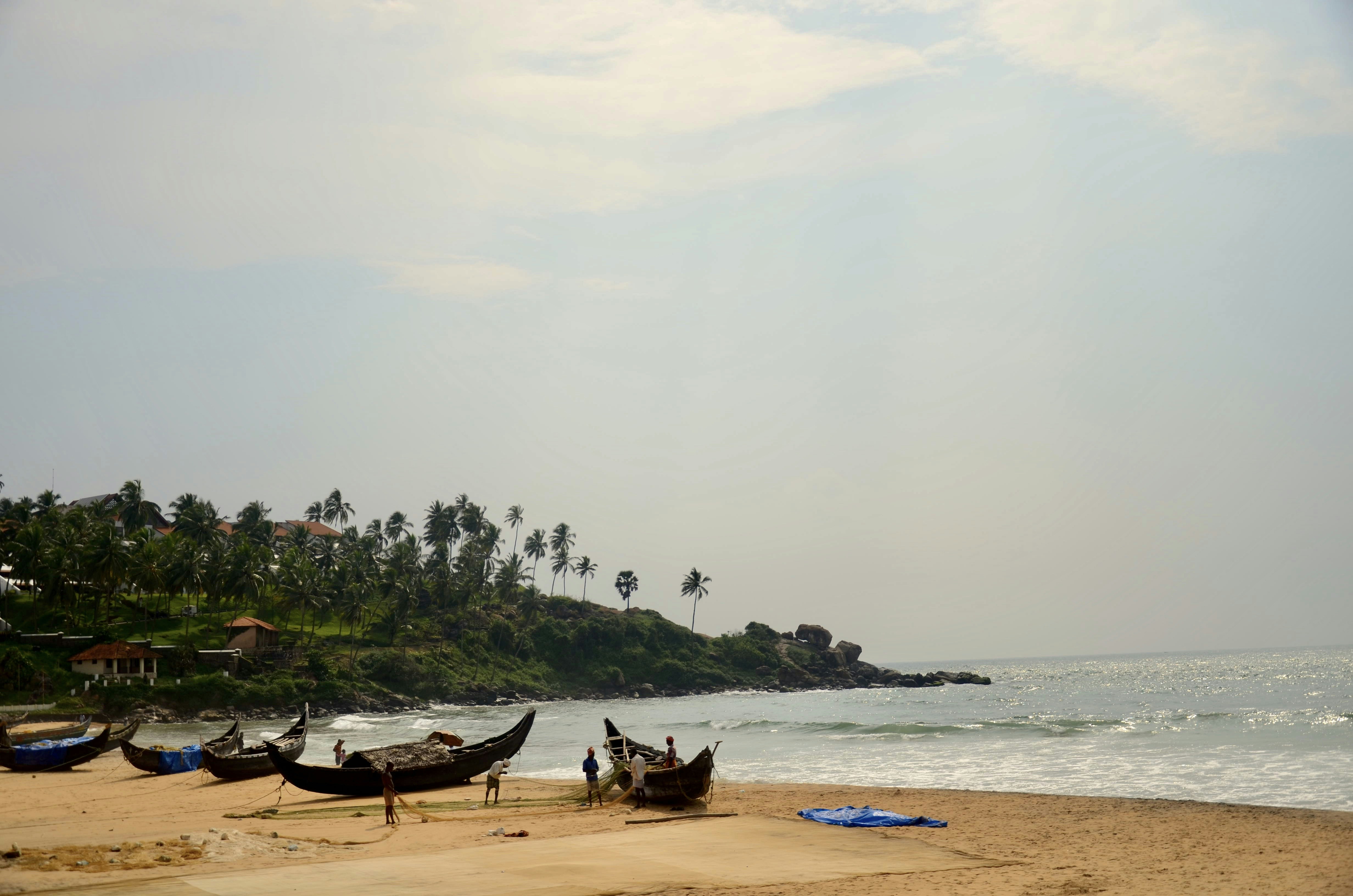Traditional fishing boats lined along the sandy beach, with lush greenery in the background and gentle waves lapping at the shore.