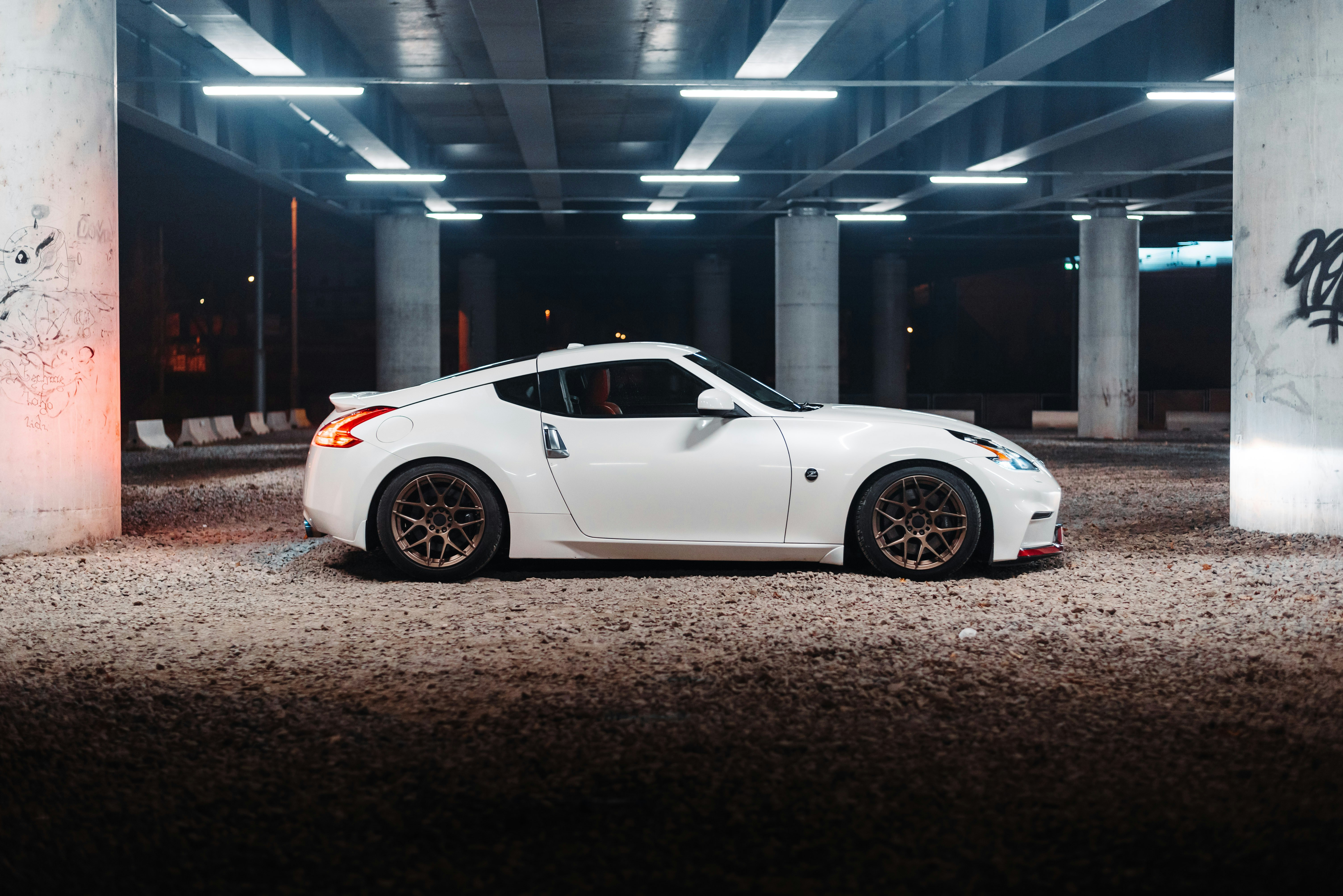 White sports car parked under a concrete structure with dramatic lighting and shadows.