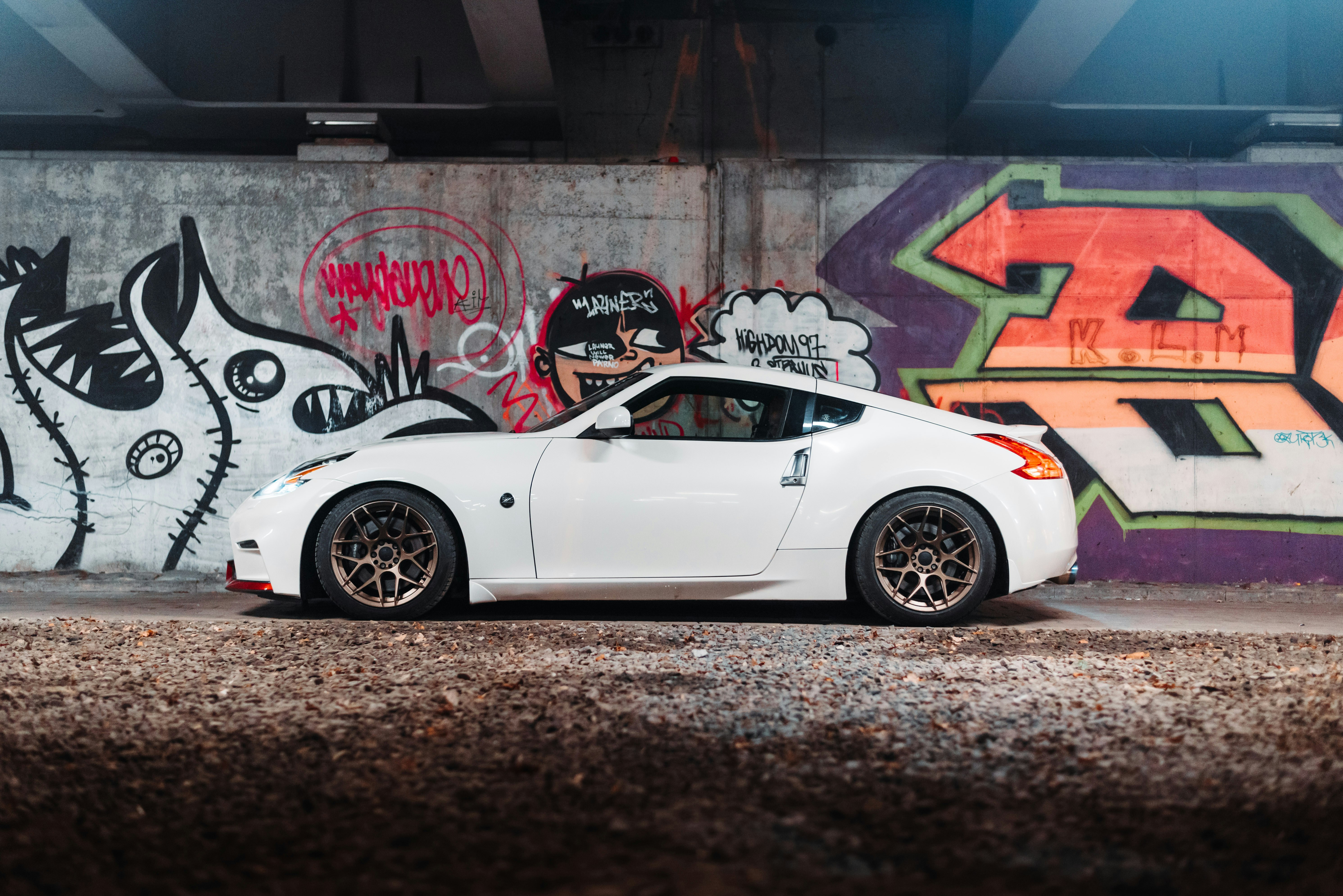 White sports car parked against a graffiti-covered wall under an overpass.