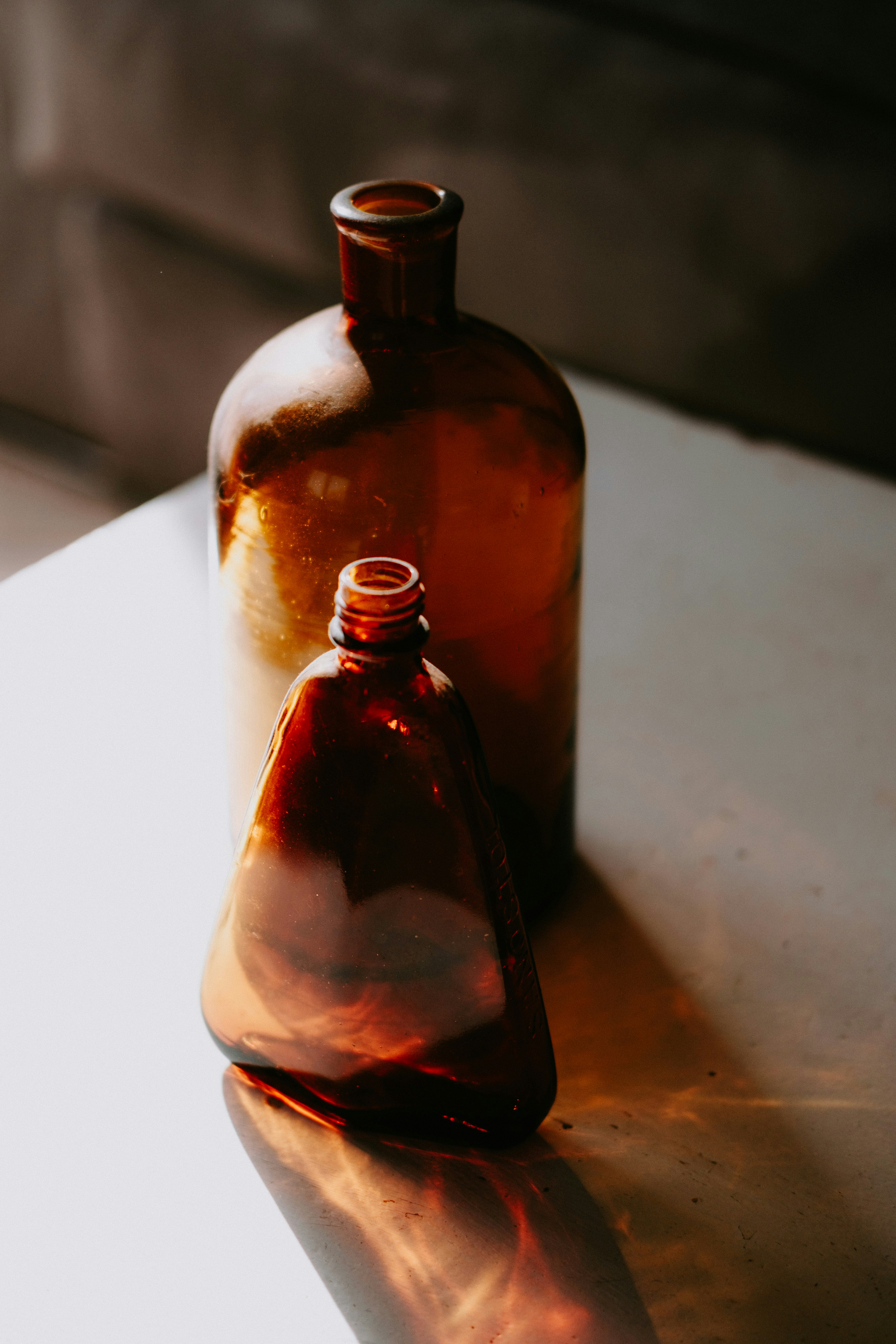 Two amber glass bottles casting reflections on a surface, showcasing their unique shapes and the interplay of light.