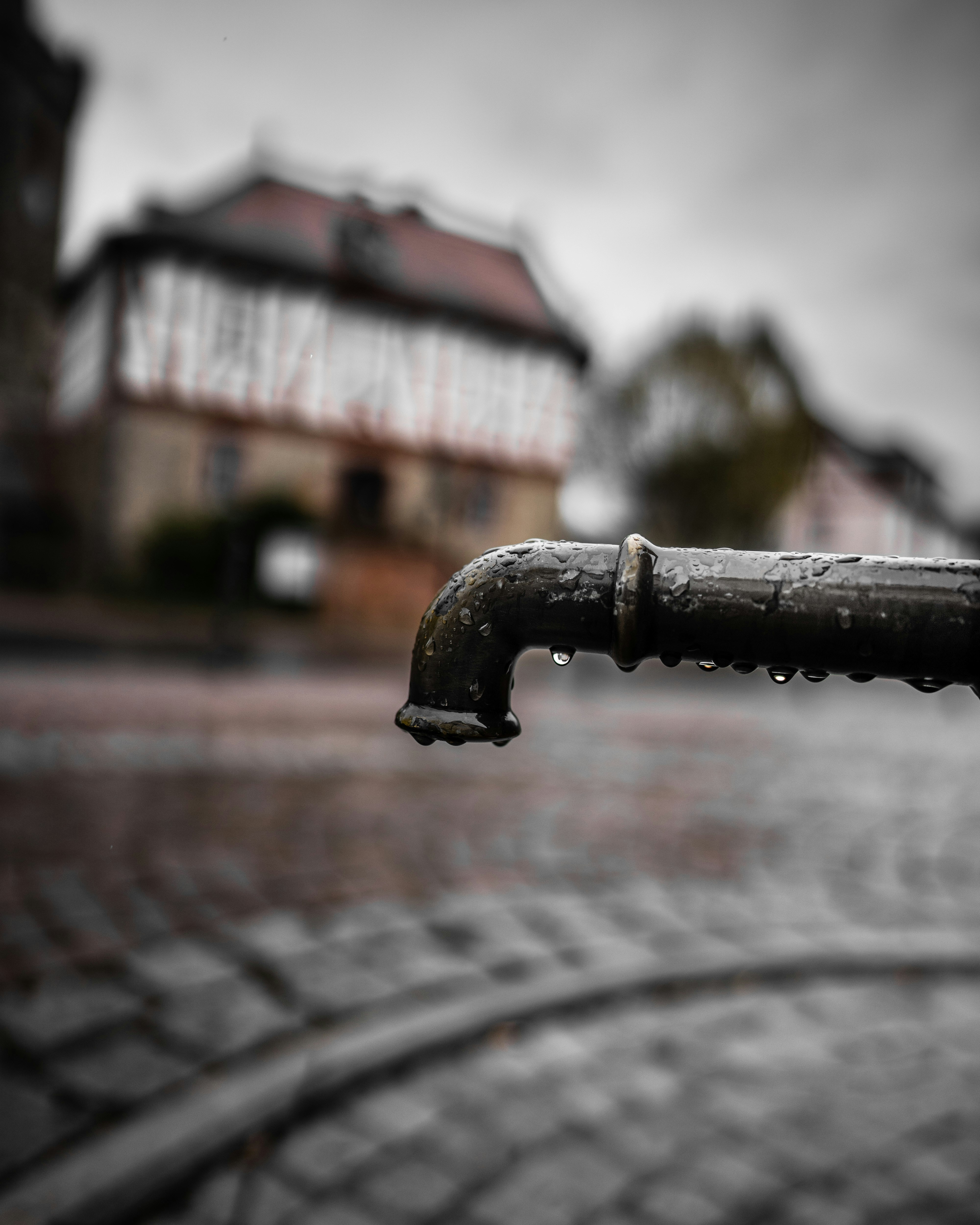 Rain Beads on a Curved Pipe Against a Blurred City Street