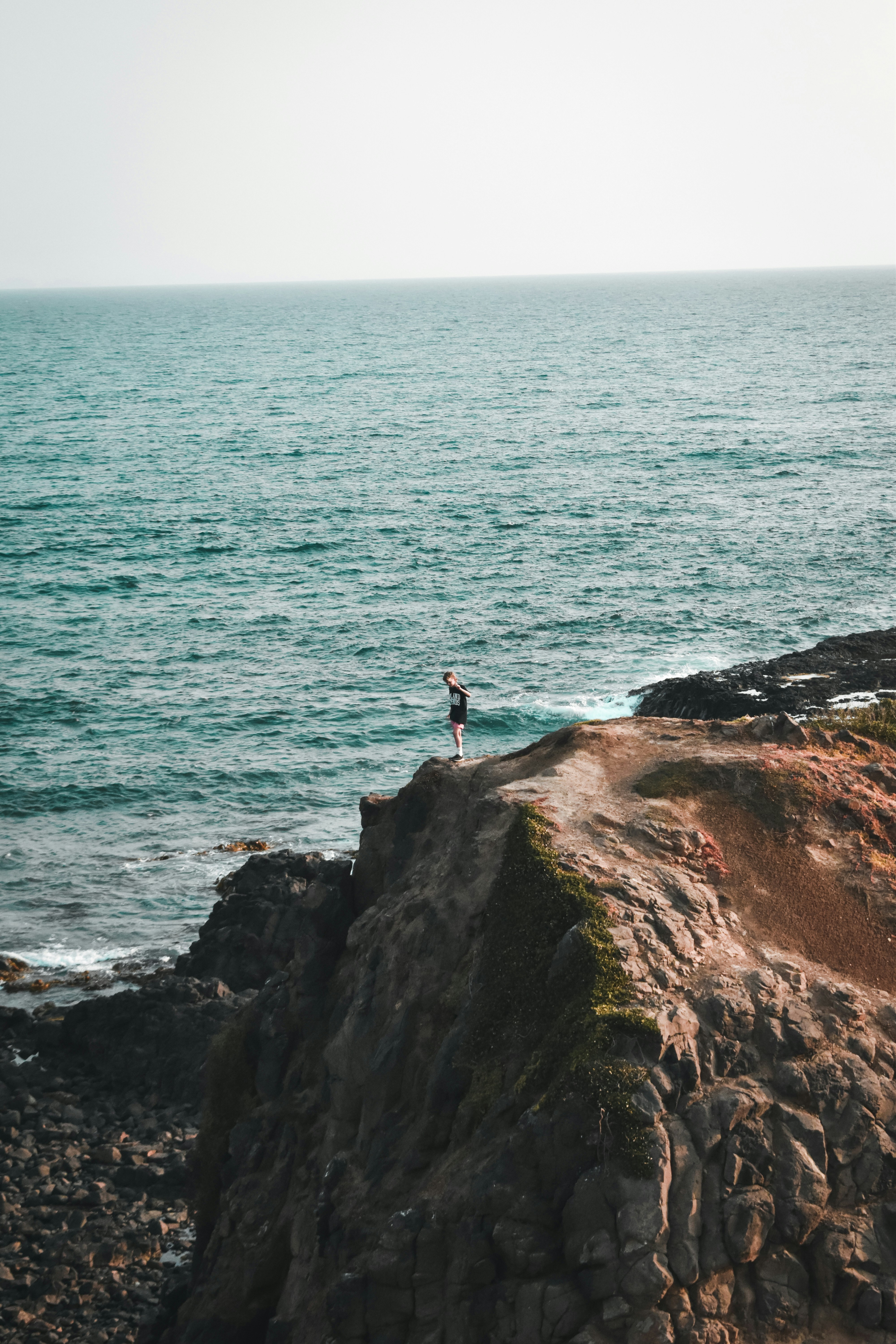 A person standing on top of a cliff near the ocean photo – Free ...