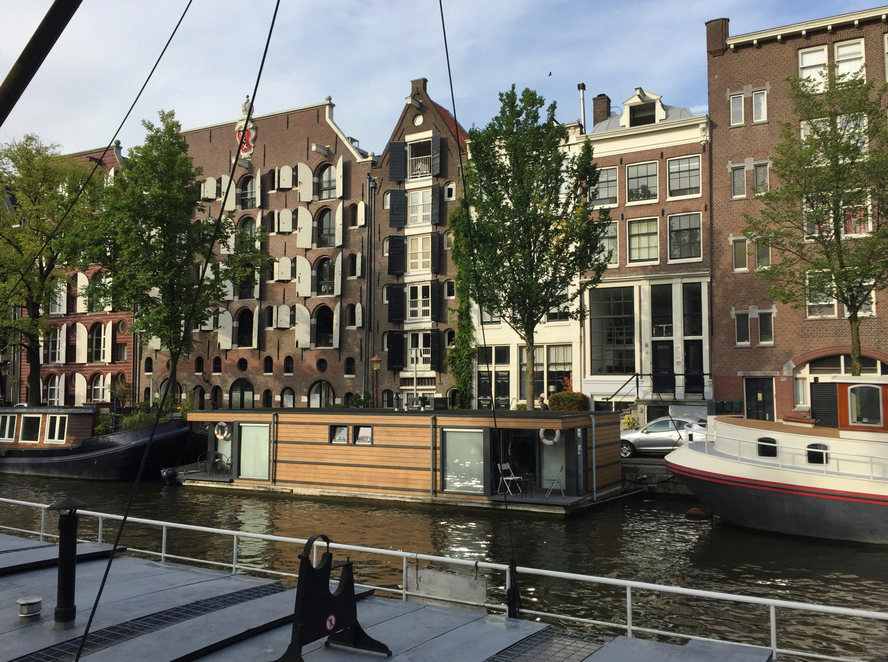 Charming houseboats line the canal, framed by historic Dutch architecture and lush greenery. The tranquil waters reflect the vibrant scene.