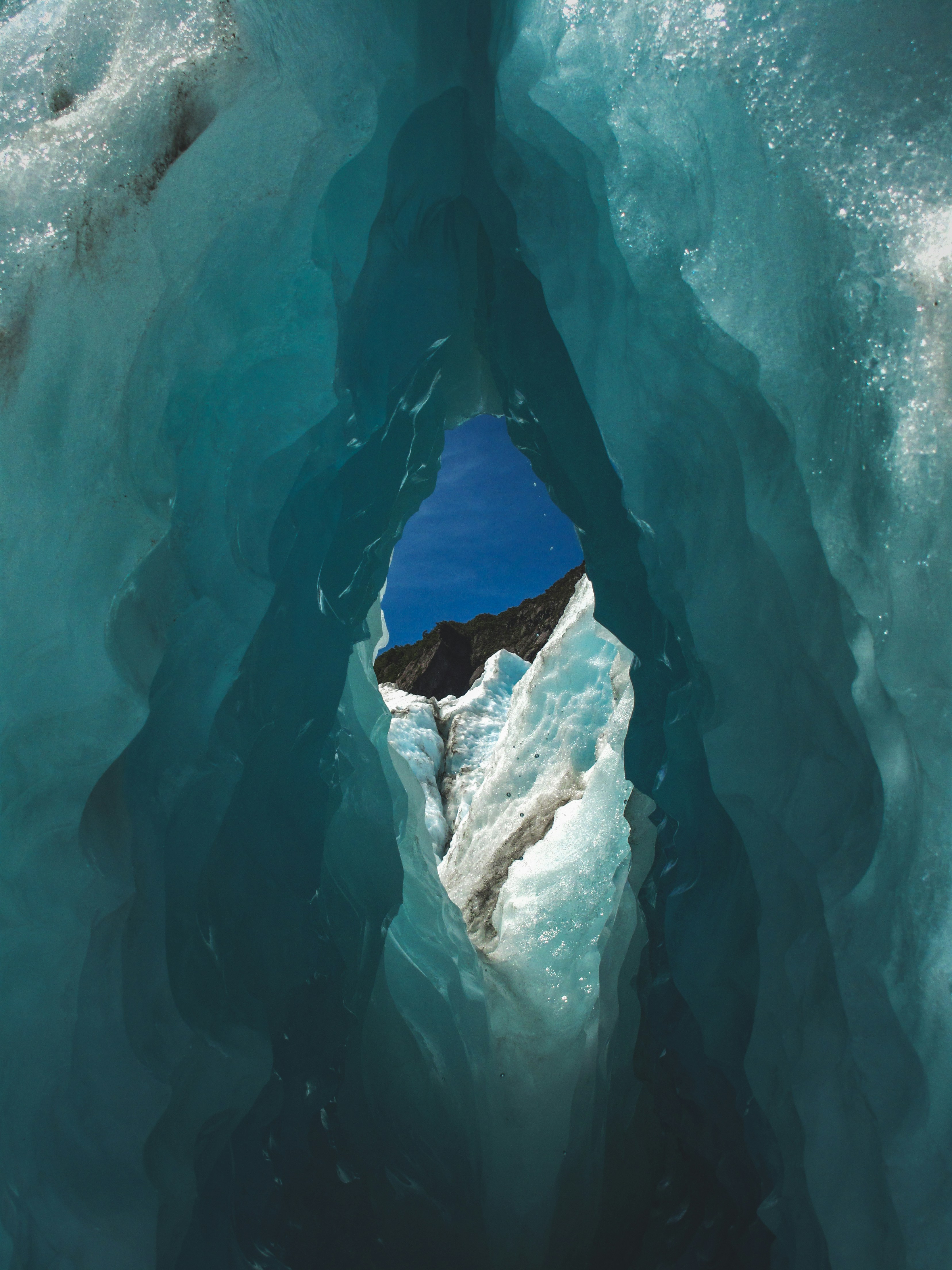 Translucent blue ice arch framing a view of a glacier and clear blue sky beyond.