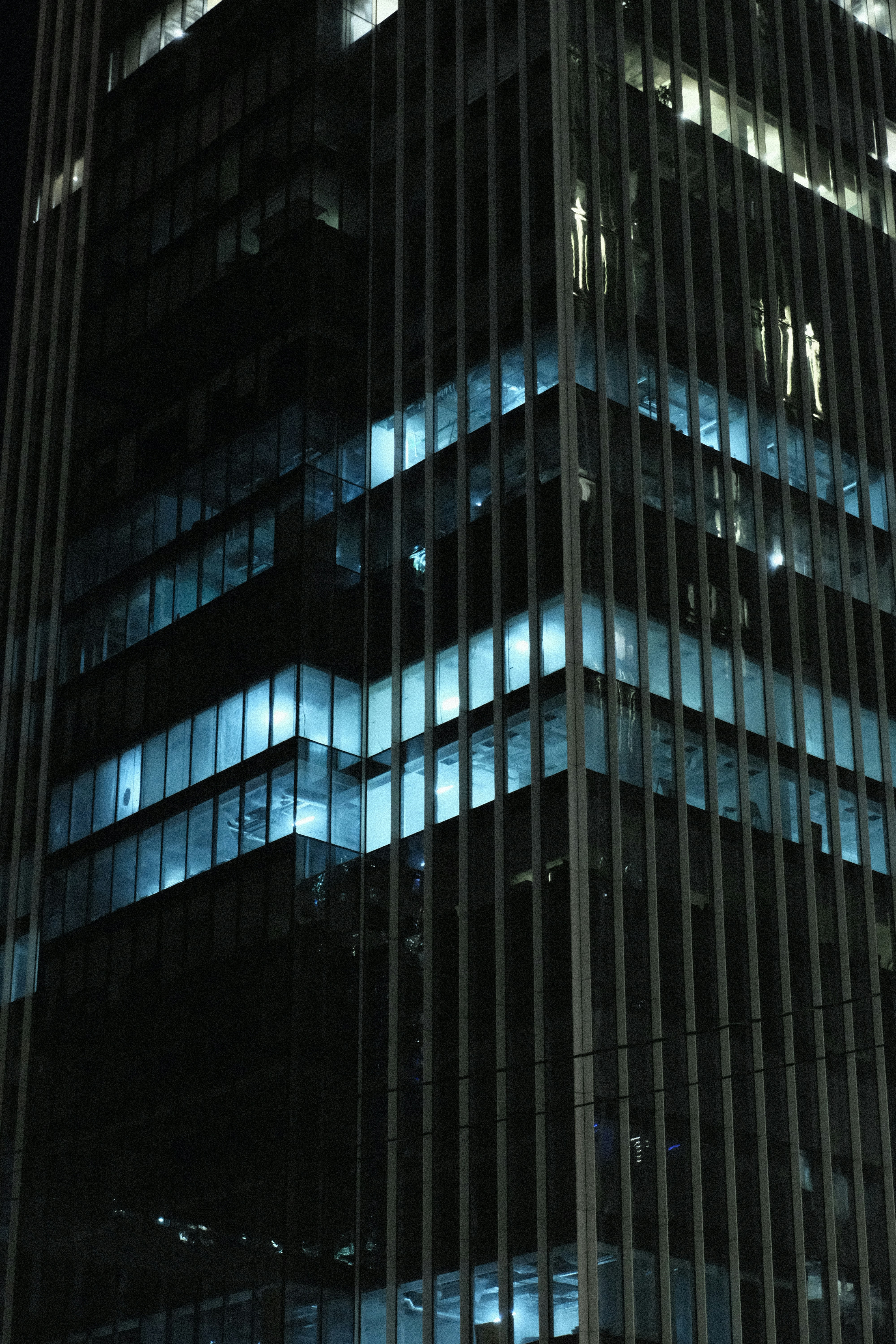 A high-rise building's glass facade illuminated by blue light, showcasing its modern architectural design at night.
