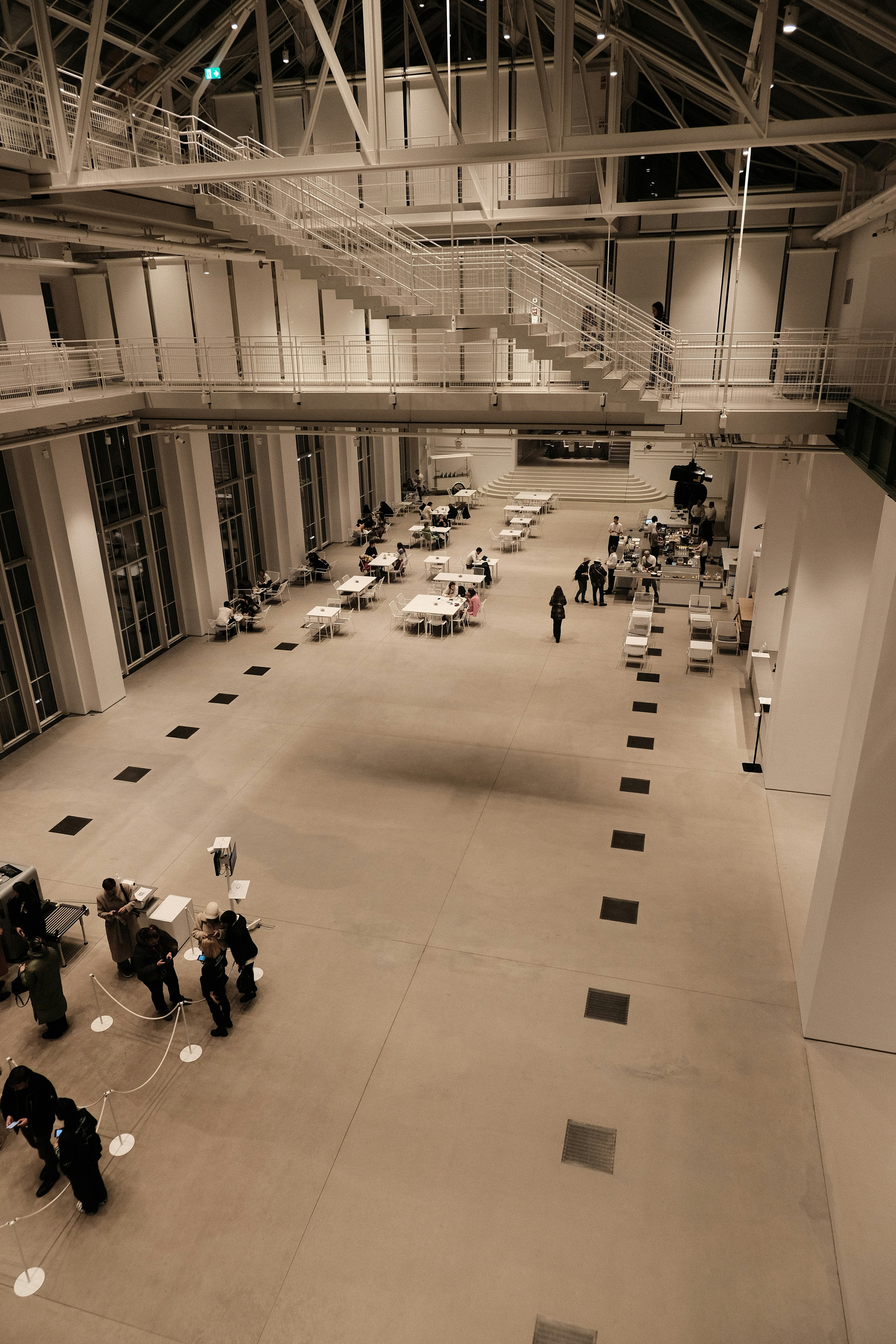Spacious modern atrium filled with tables and people, showcasing an architectural blend of light and structure. The scene captures the essence of contemporary design.