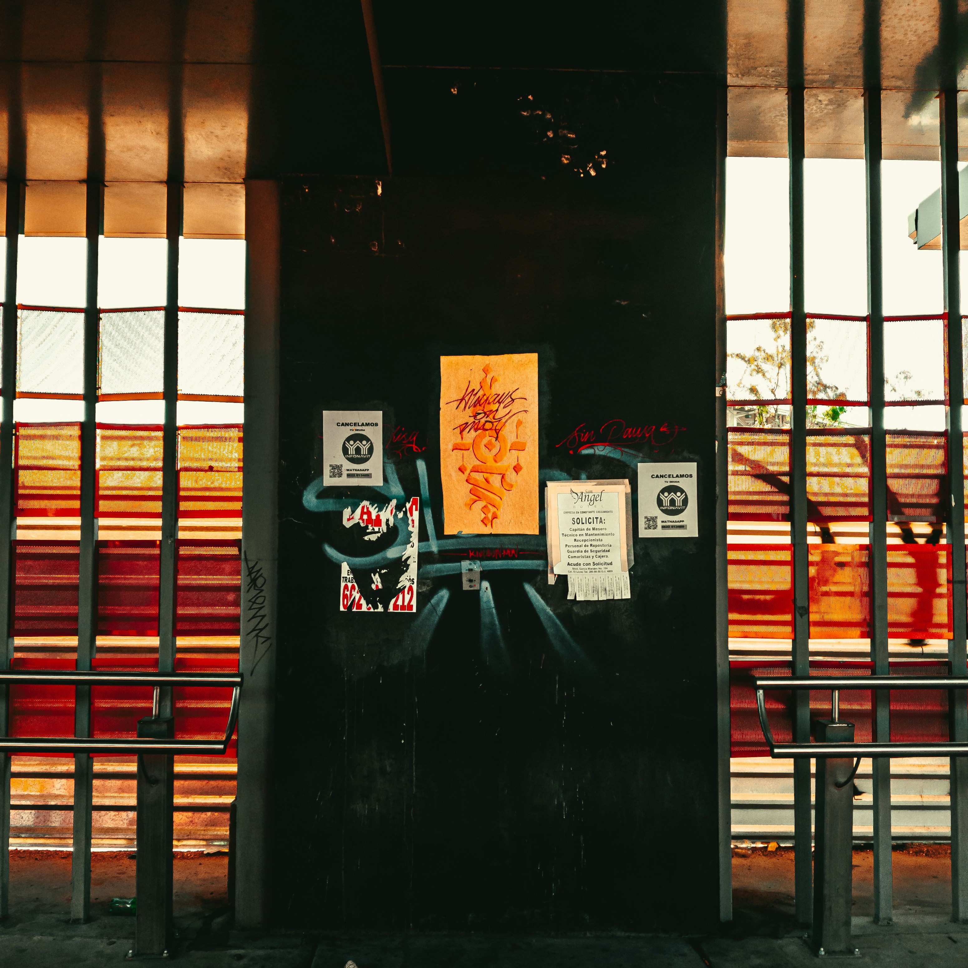 Central dark doorway covered with posters sits between sunlit slatted walls in a quiet transit hall. The warm light and linear perspective emphasize the doorway as the scene's focal point.