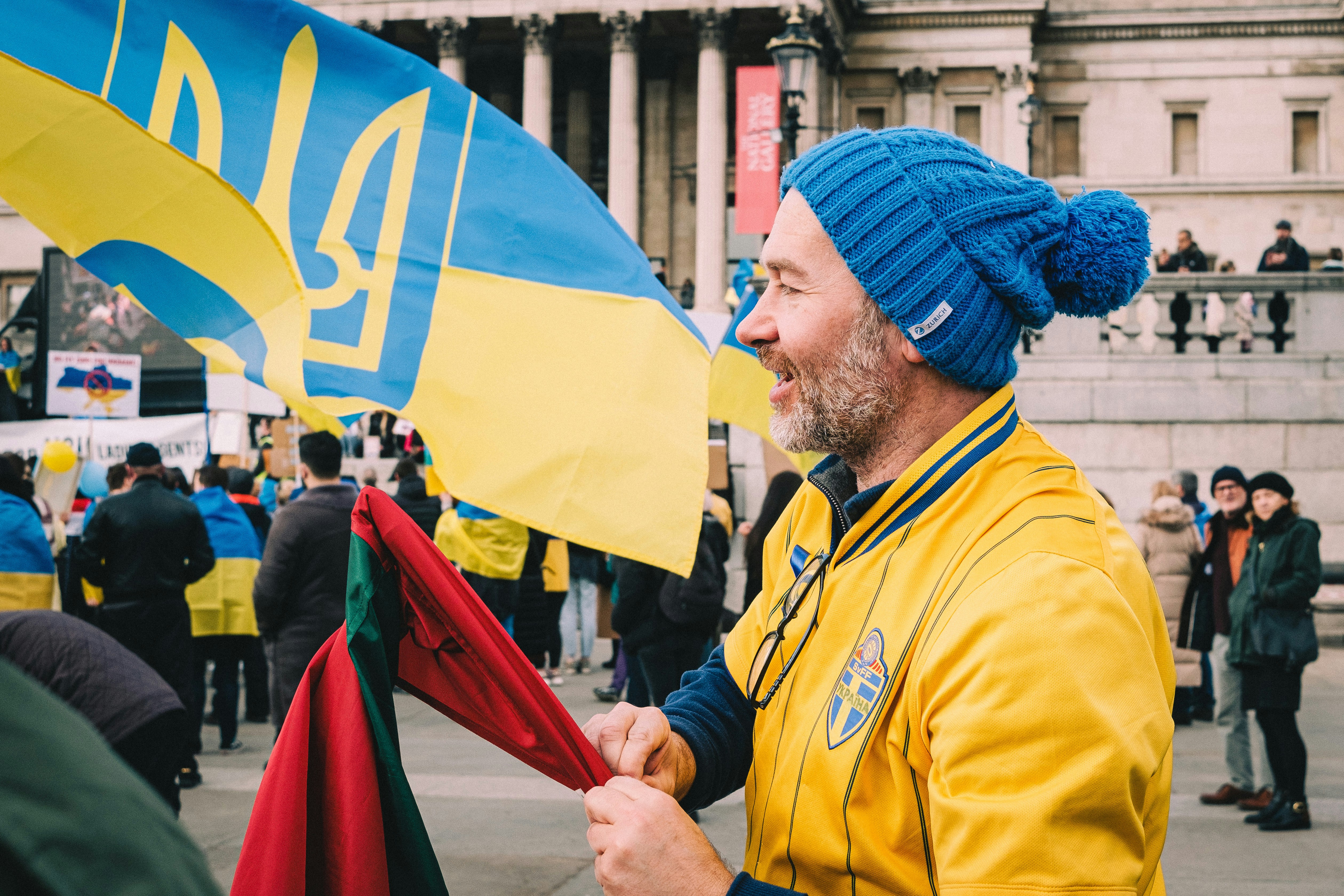 A man in a yellow jacket holding a blue and yellow flag photo – Free ...