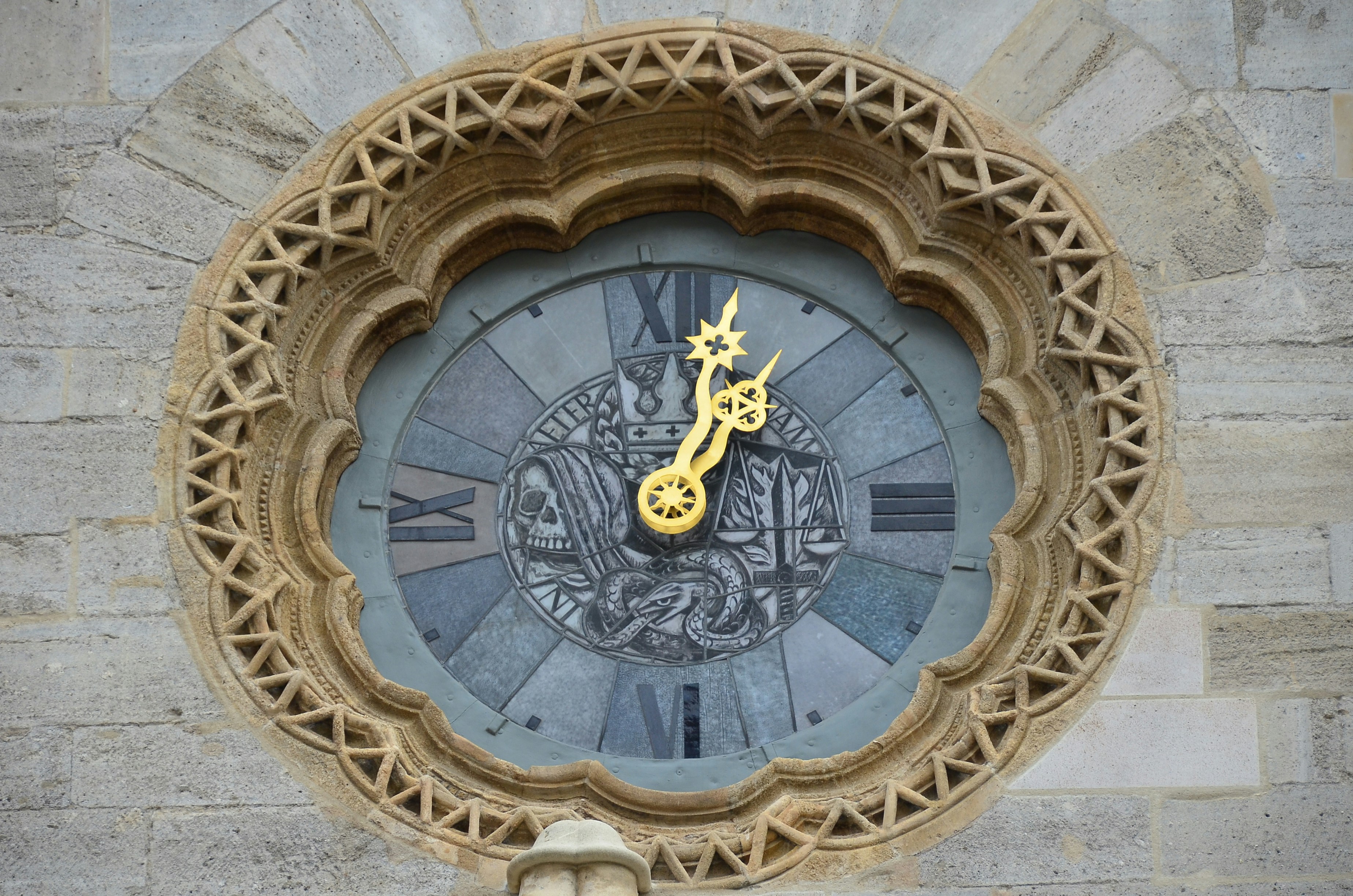 Intricate clock face featuring ornate design and gold accents, showcasing Roman numerals and a detailed background motif.
