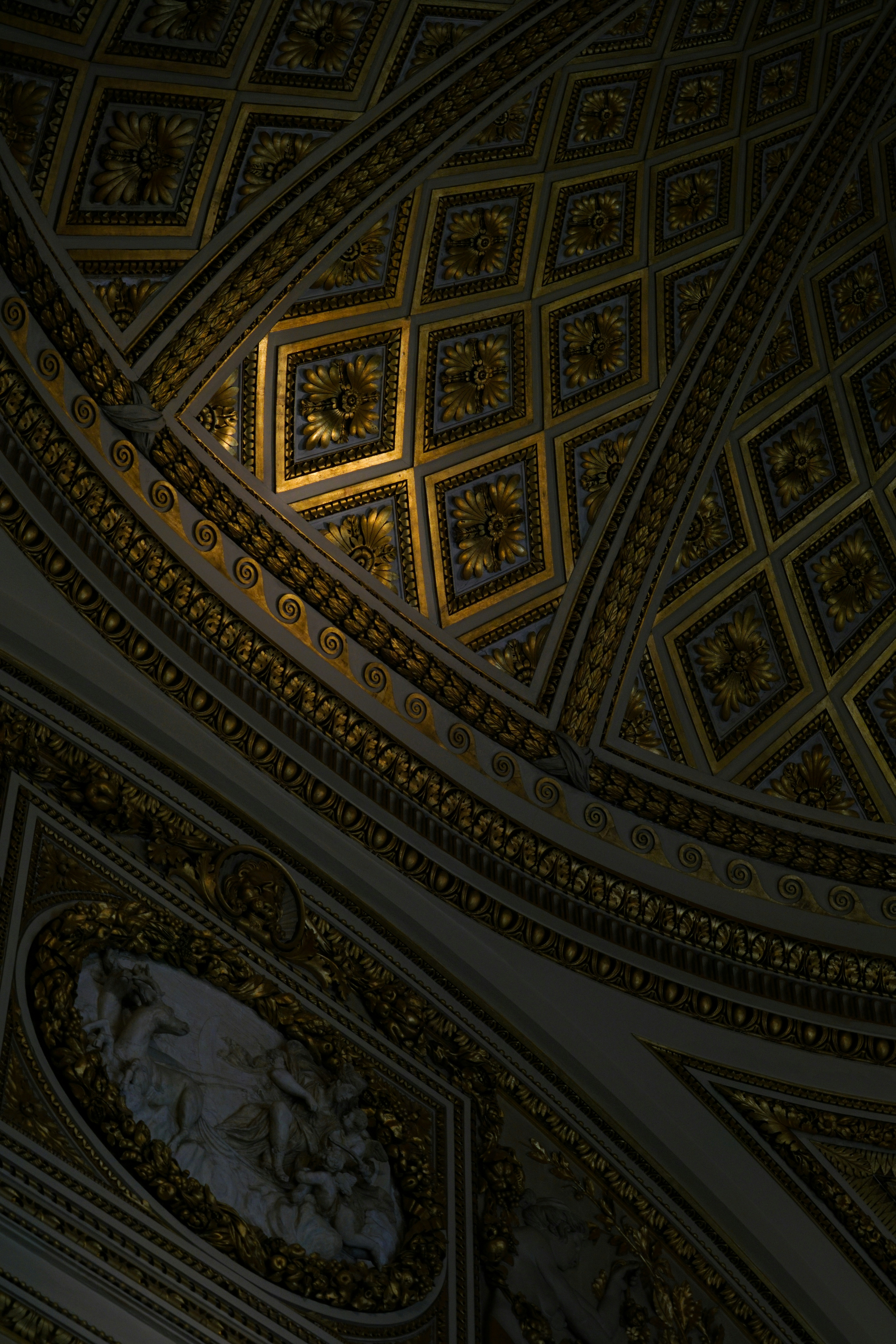 Intricate gold and blue ceiling design featuring ornate floral motifs and classical sculptures in a richly decorated interior.