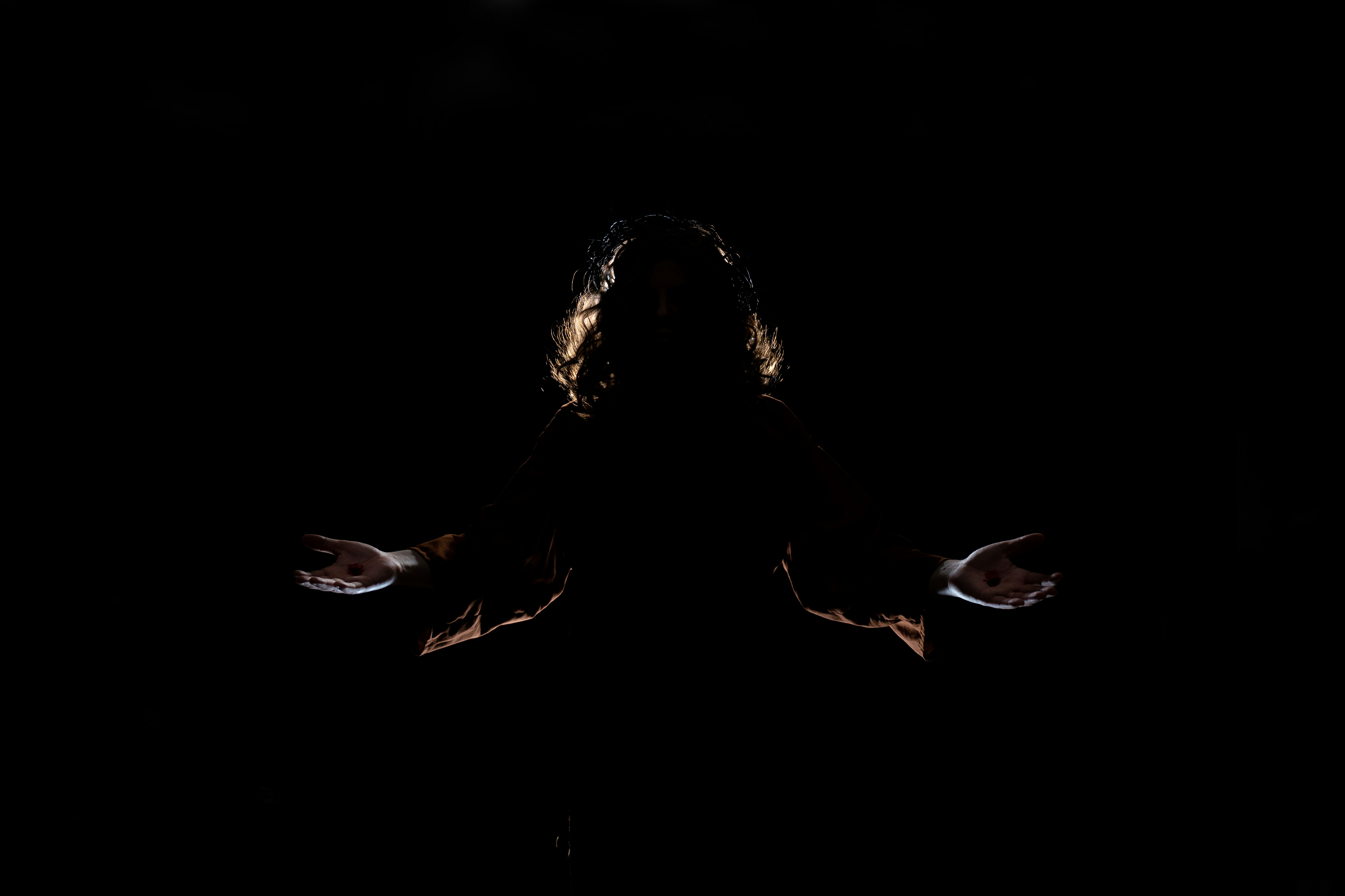 Silhouetted figure with outstretched arms, illuminated by subtle light against a dark backdrop.
