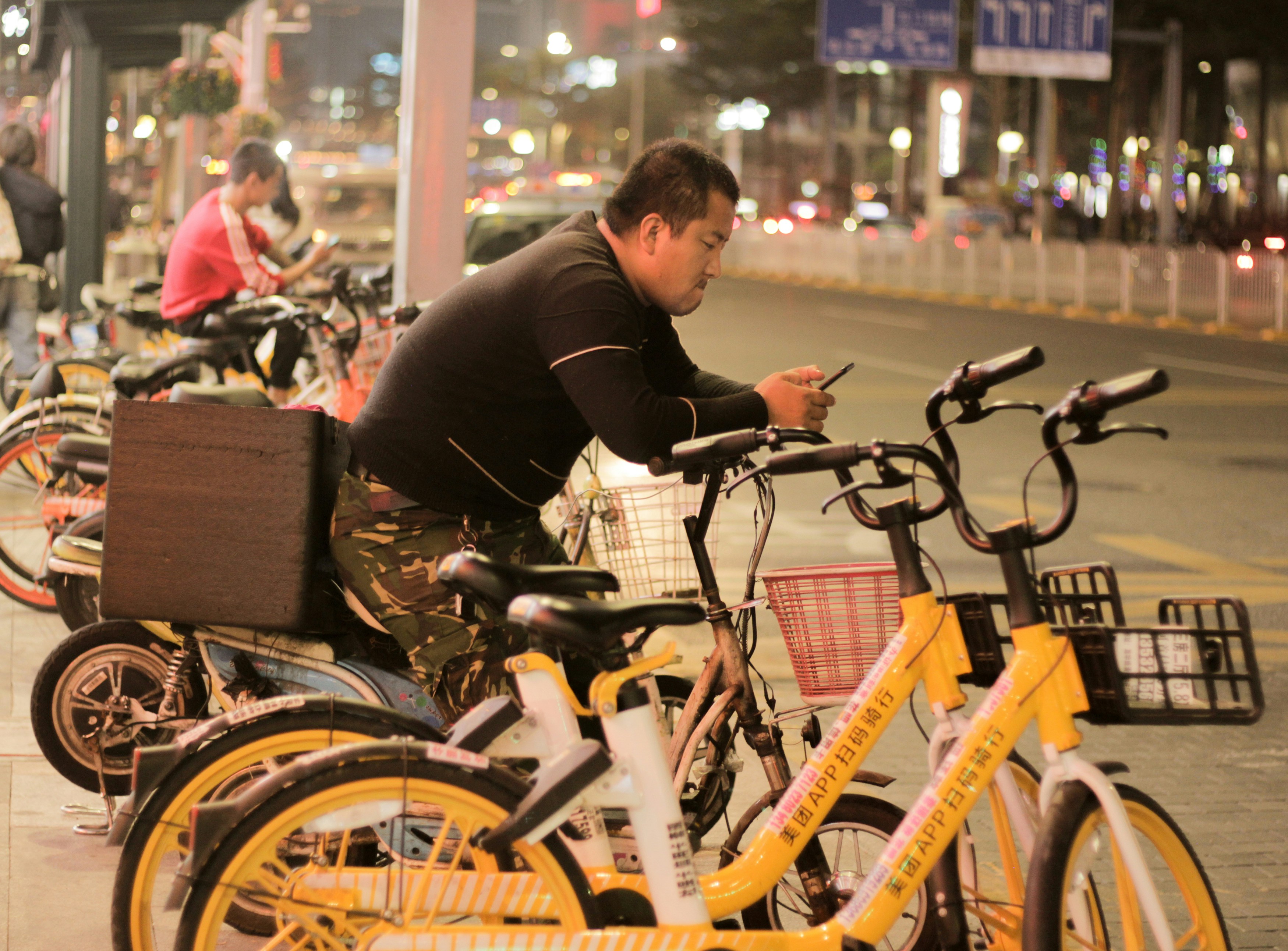 Night Market Pause: A man with a phone among yellow bicycles under city glow