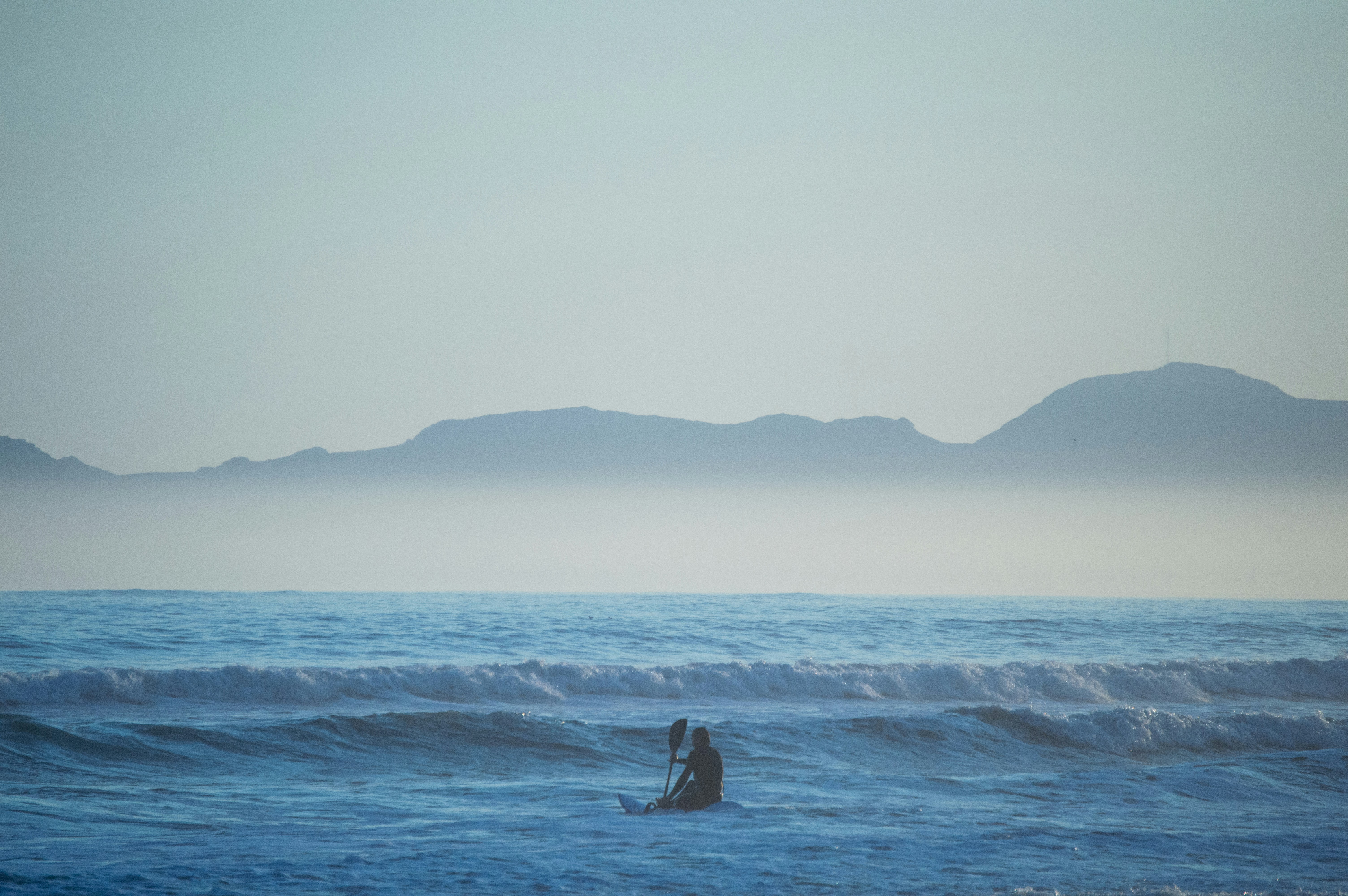 Two surfers riding a wave in a serene ocean setting with distant hills.