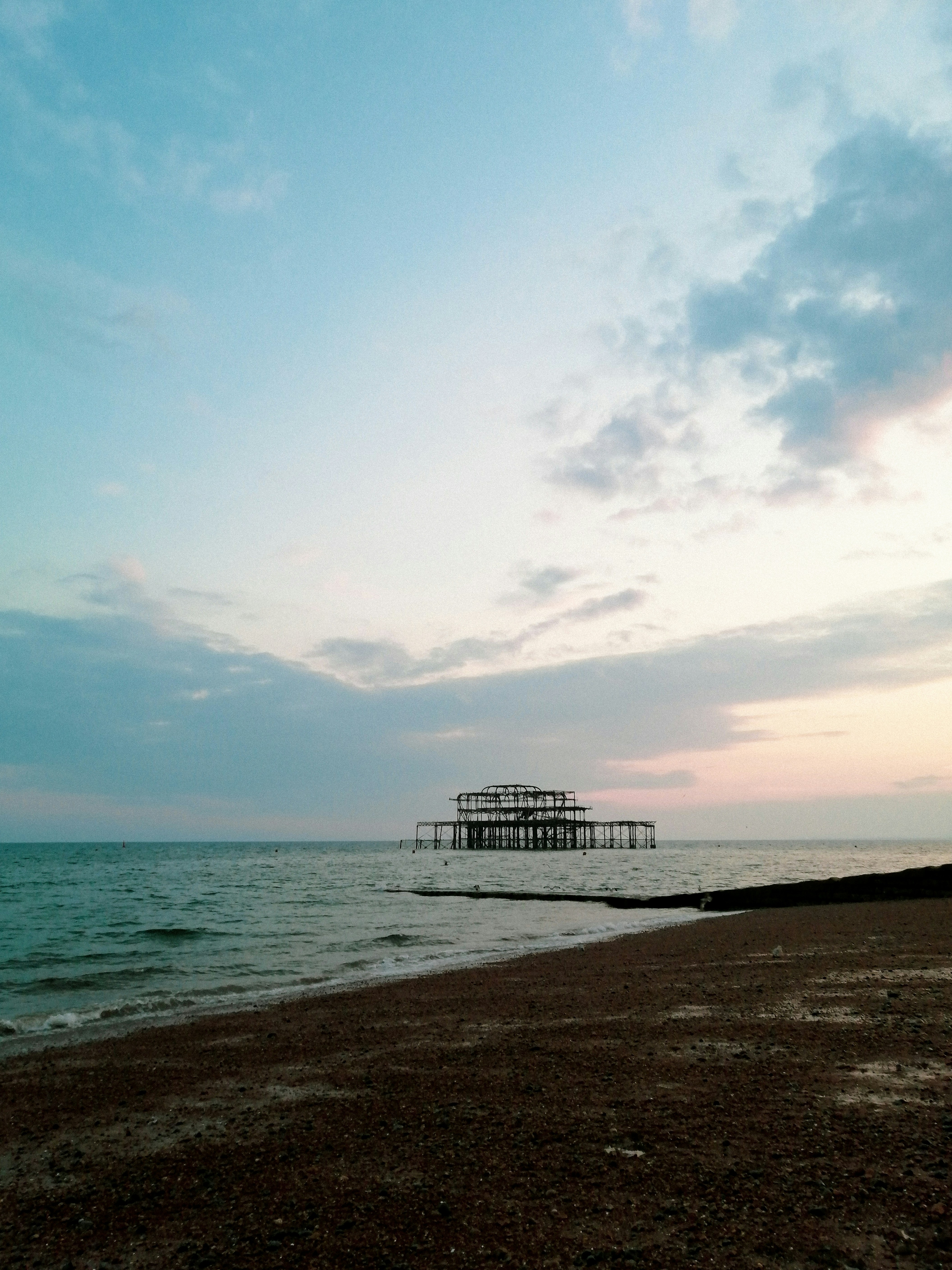 Ruins of a once-vibrant pier emerging from the calm sea at dusk, framed by a pastel sky.