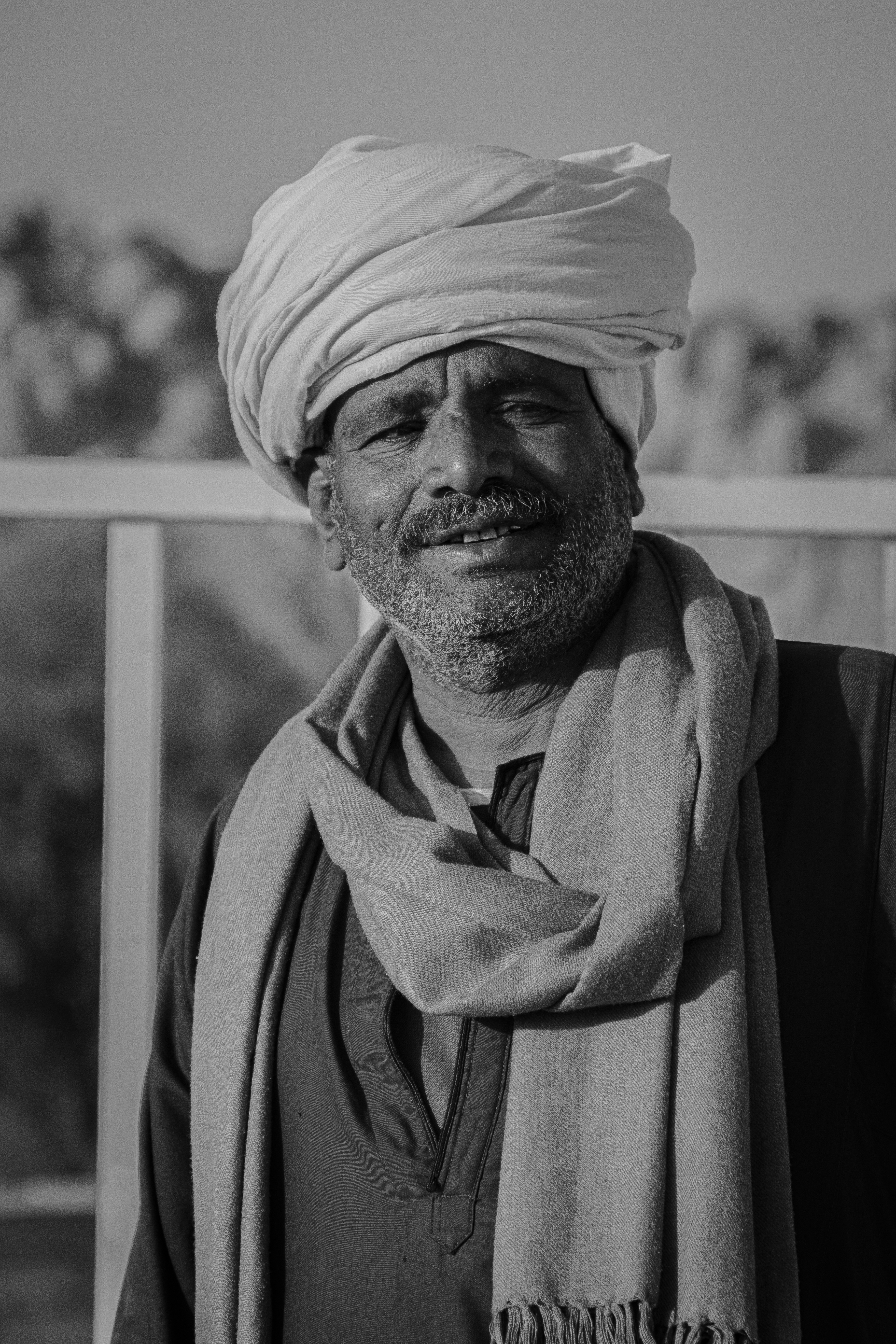 Elderly man wearing a traditional turban and scarf, exuding a sense of wisdom and warmth against a blurred background.