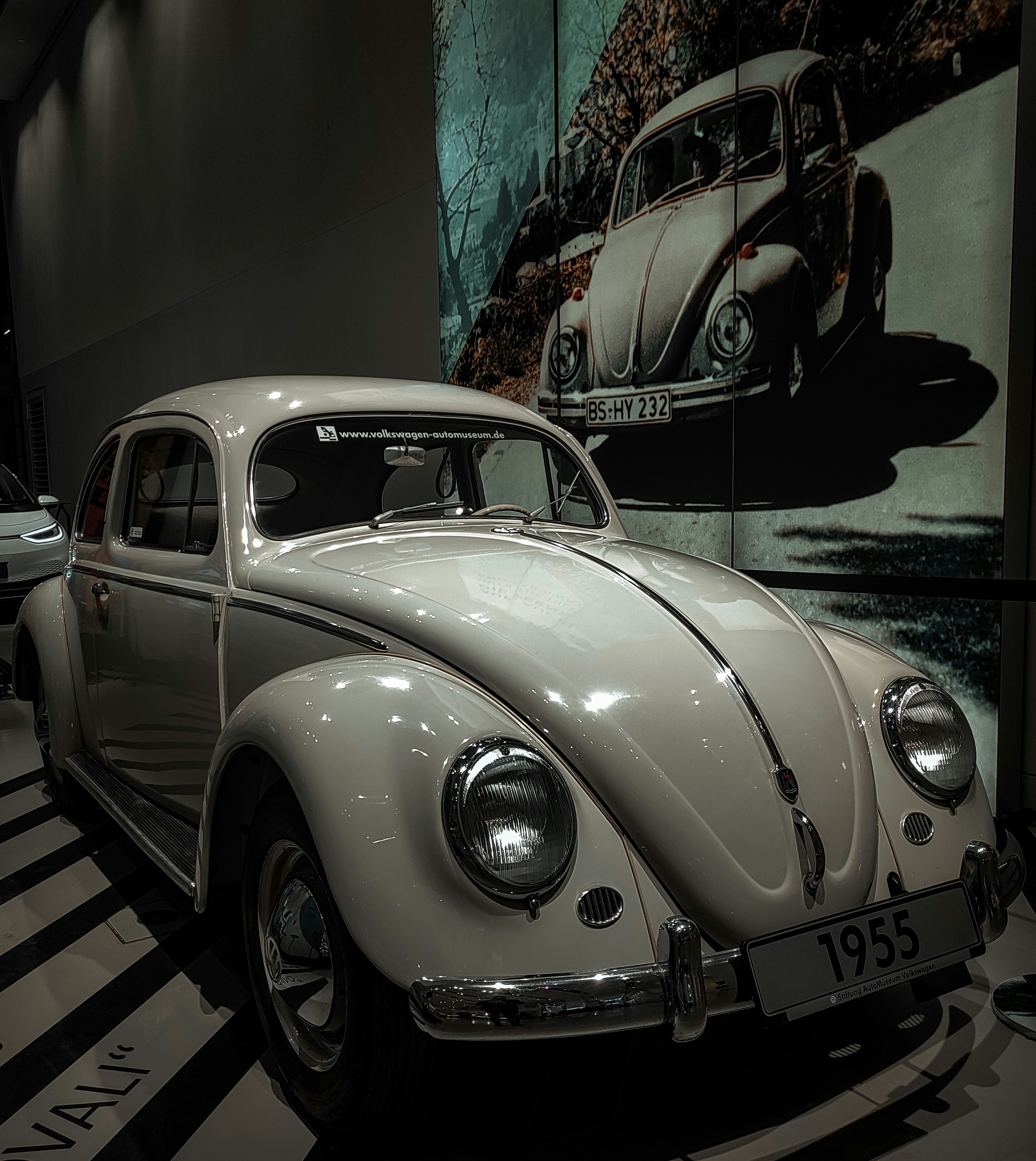 Vintage Volkswagen Beetle displayed prominently against a retro backdrop. The car is a 1955 model, showcasing its iconic design.