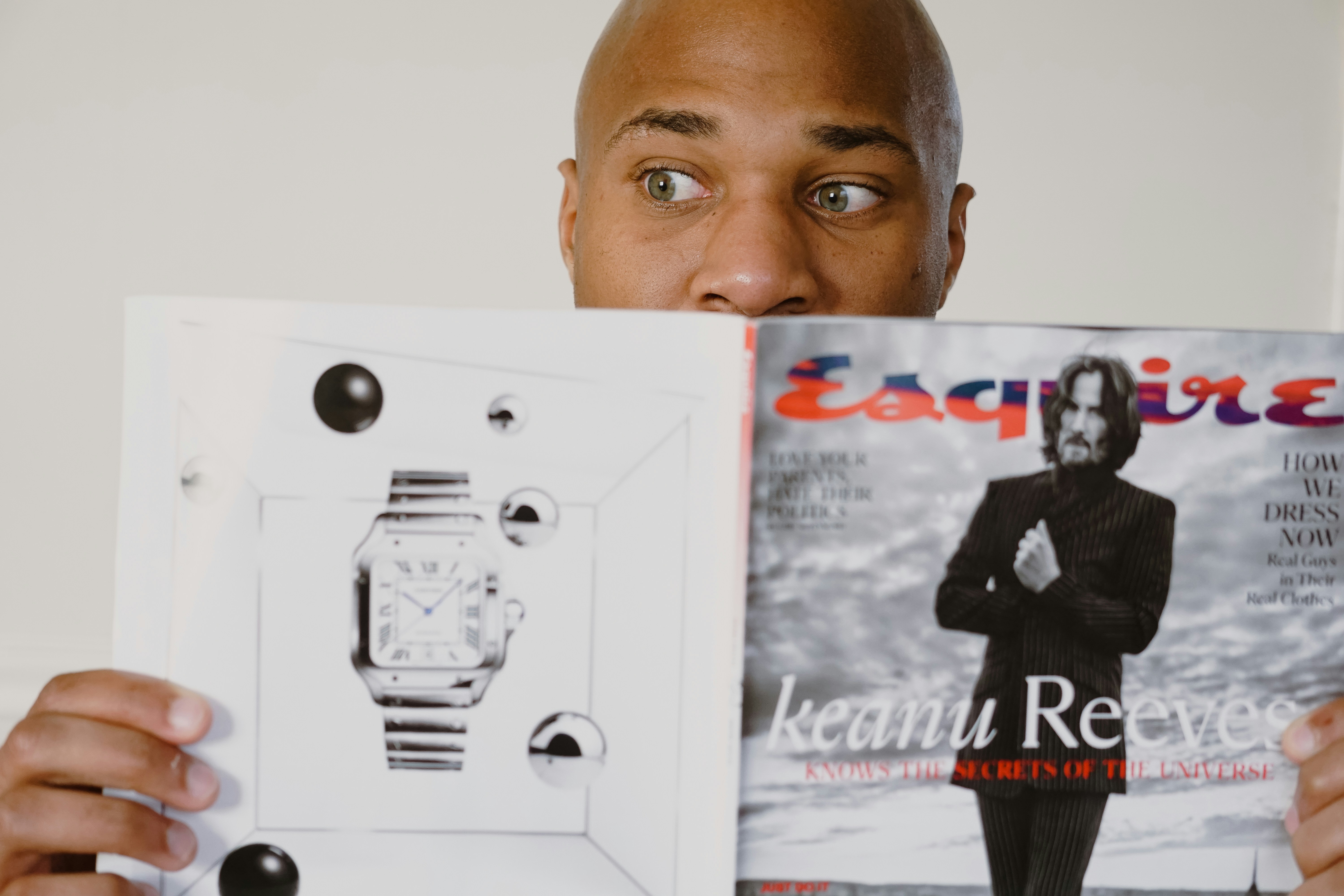 A man holds an Esquire magazine featuring Keanu Reeves while partially obscuring a sketch of a watch. The focus is on the intriguing juxtaposition of fashion and celebrity.