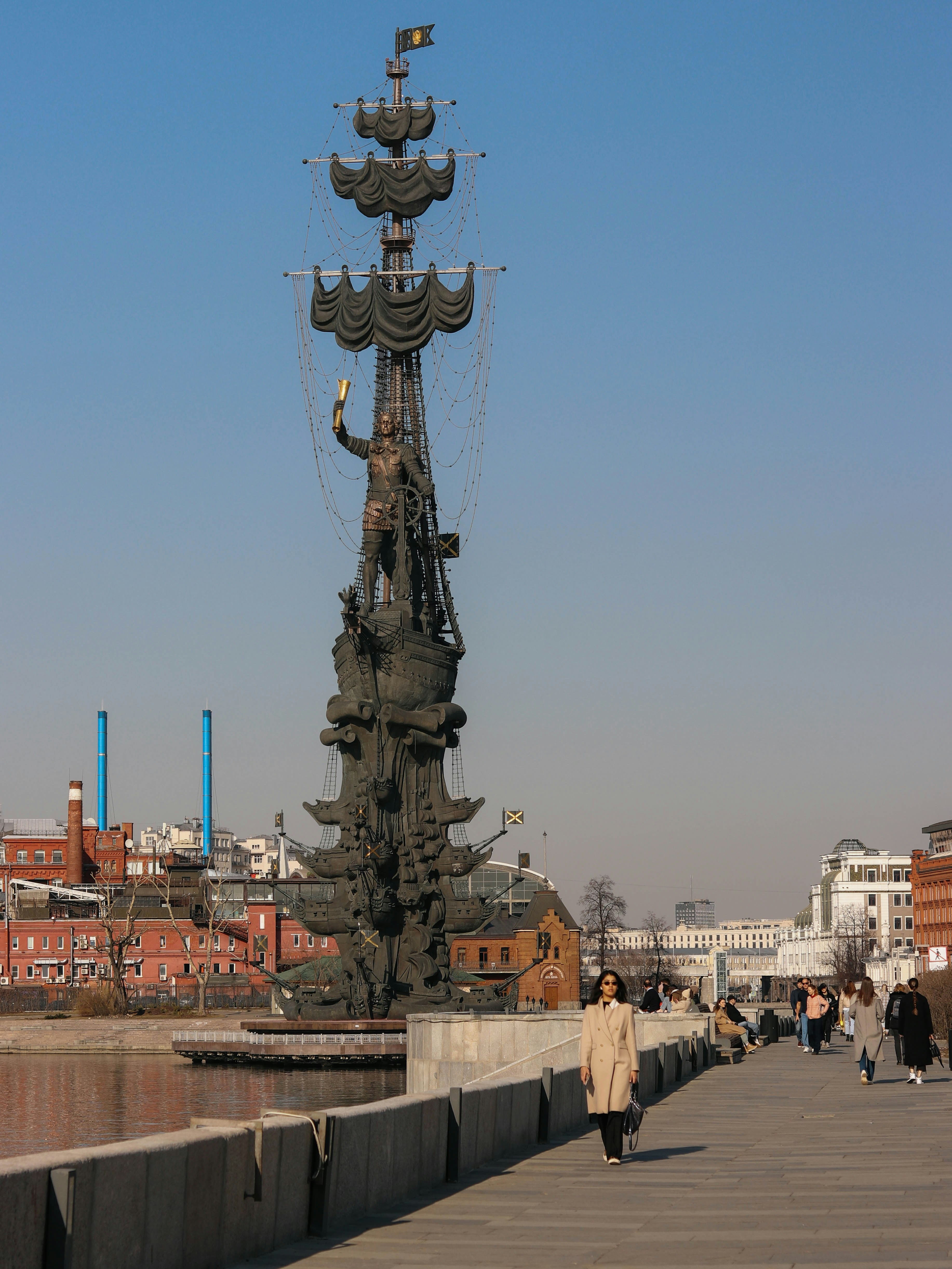 Monumental statue of a historic figure atop a ship-like structure, surrounded by a bustling waterfront promenade.