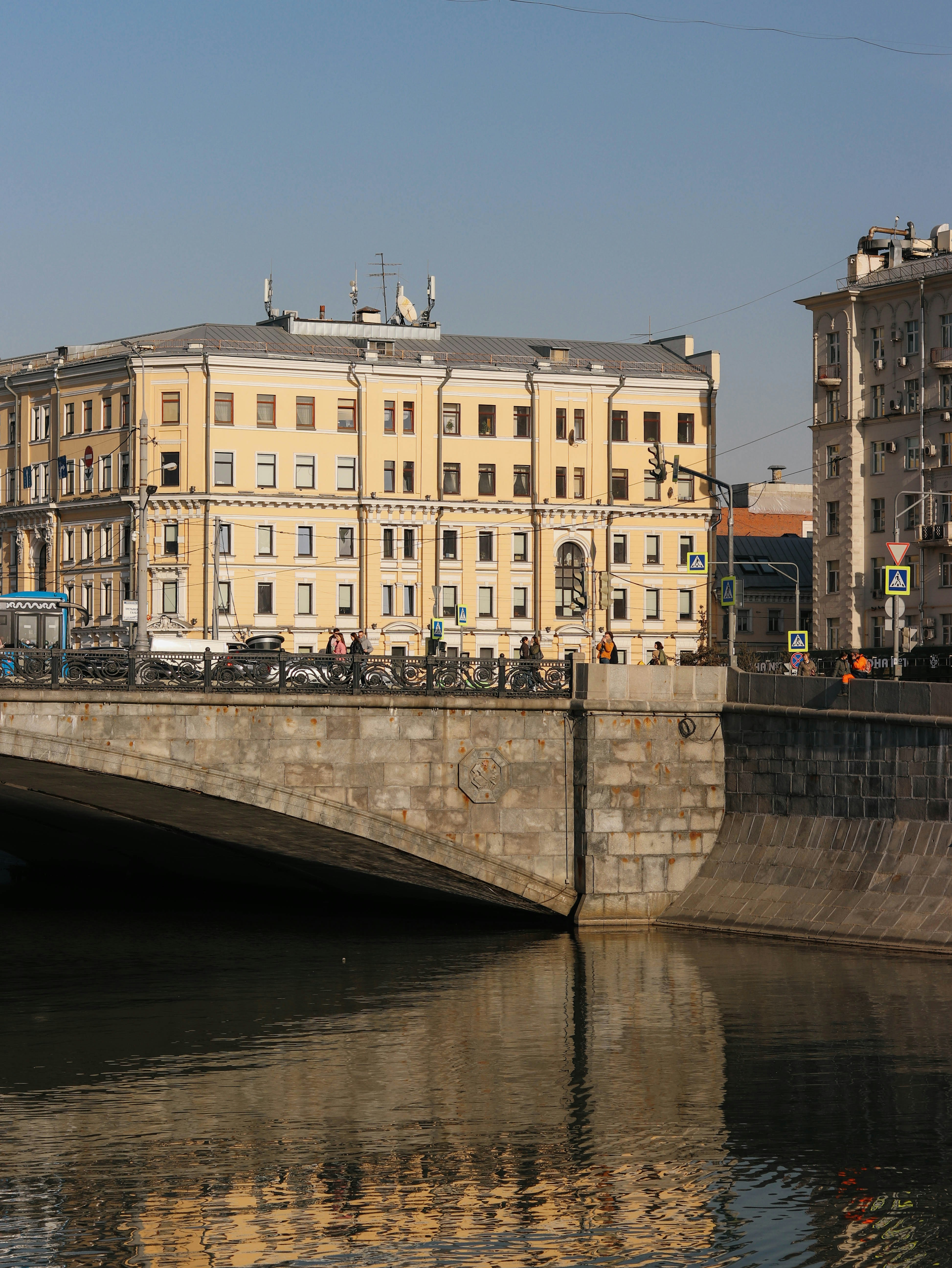 Historic stone bridge connecting vibrant buildings along a city river, with clear reflections and pedestrians enjoying the day.