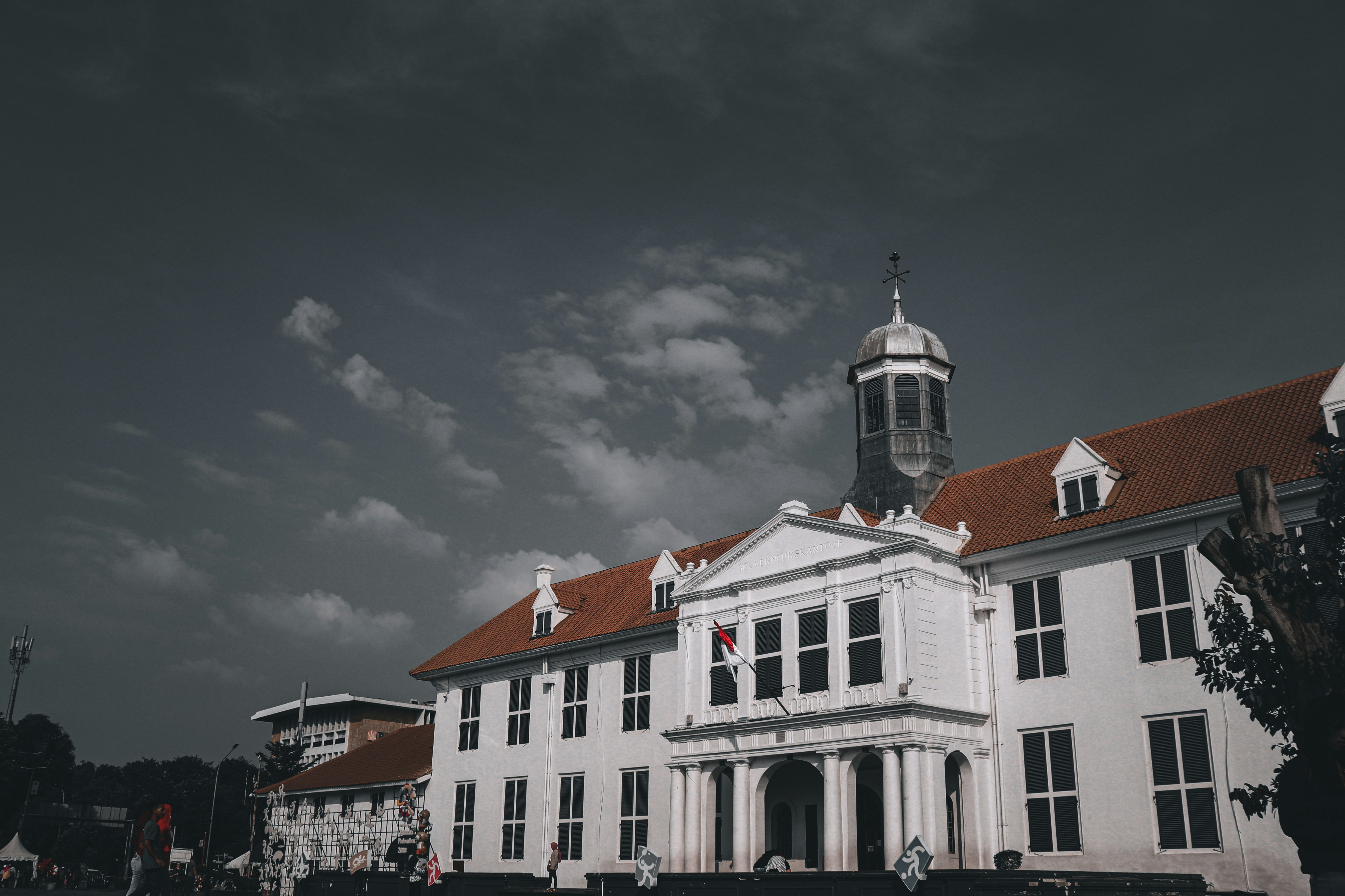 Large white building with a red roof and central clock tower beneath a cloudy sky.