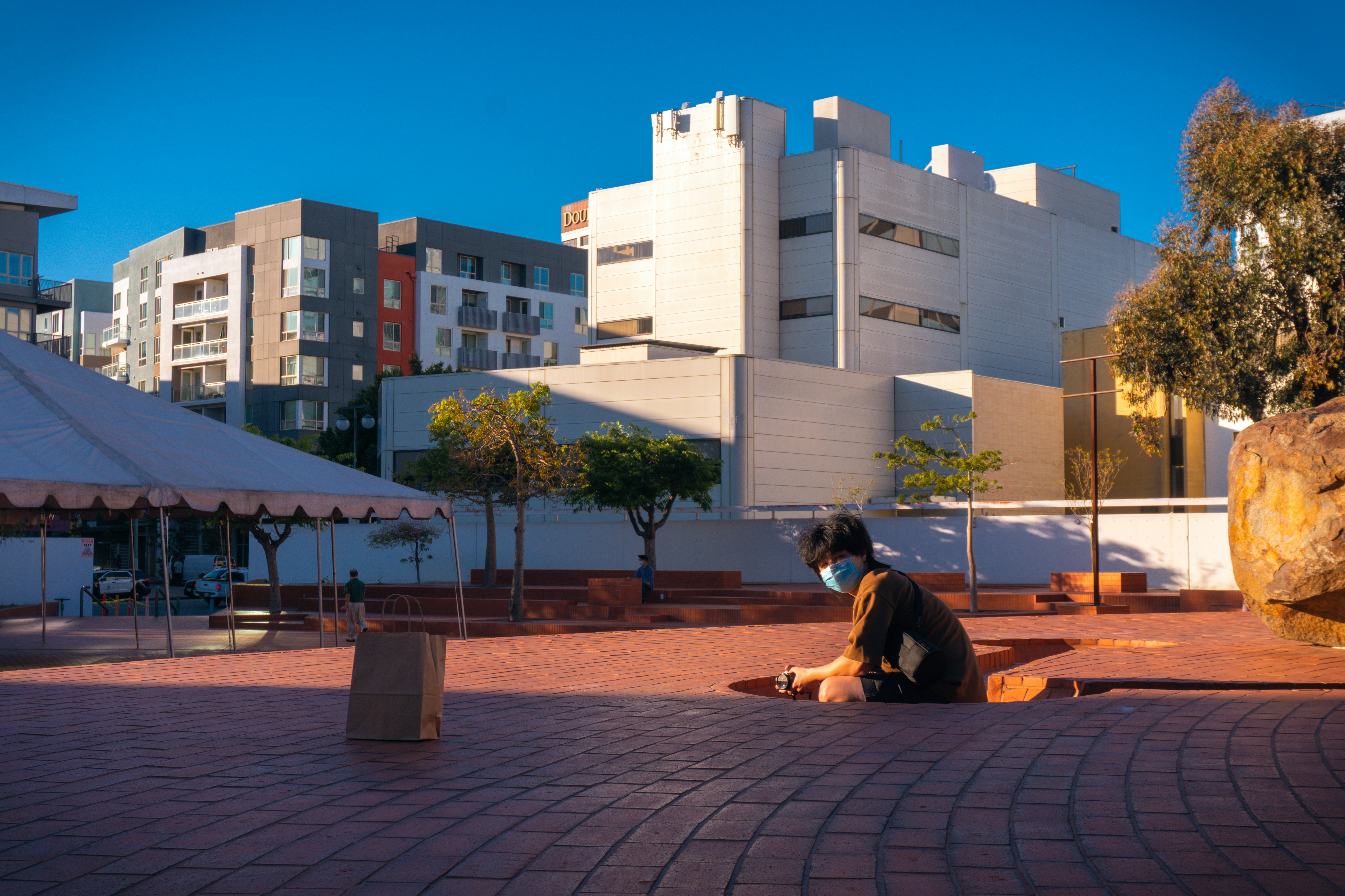 Sunlit Stillness: A Masked Figure in the Modern Square