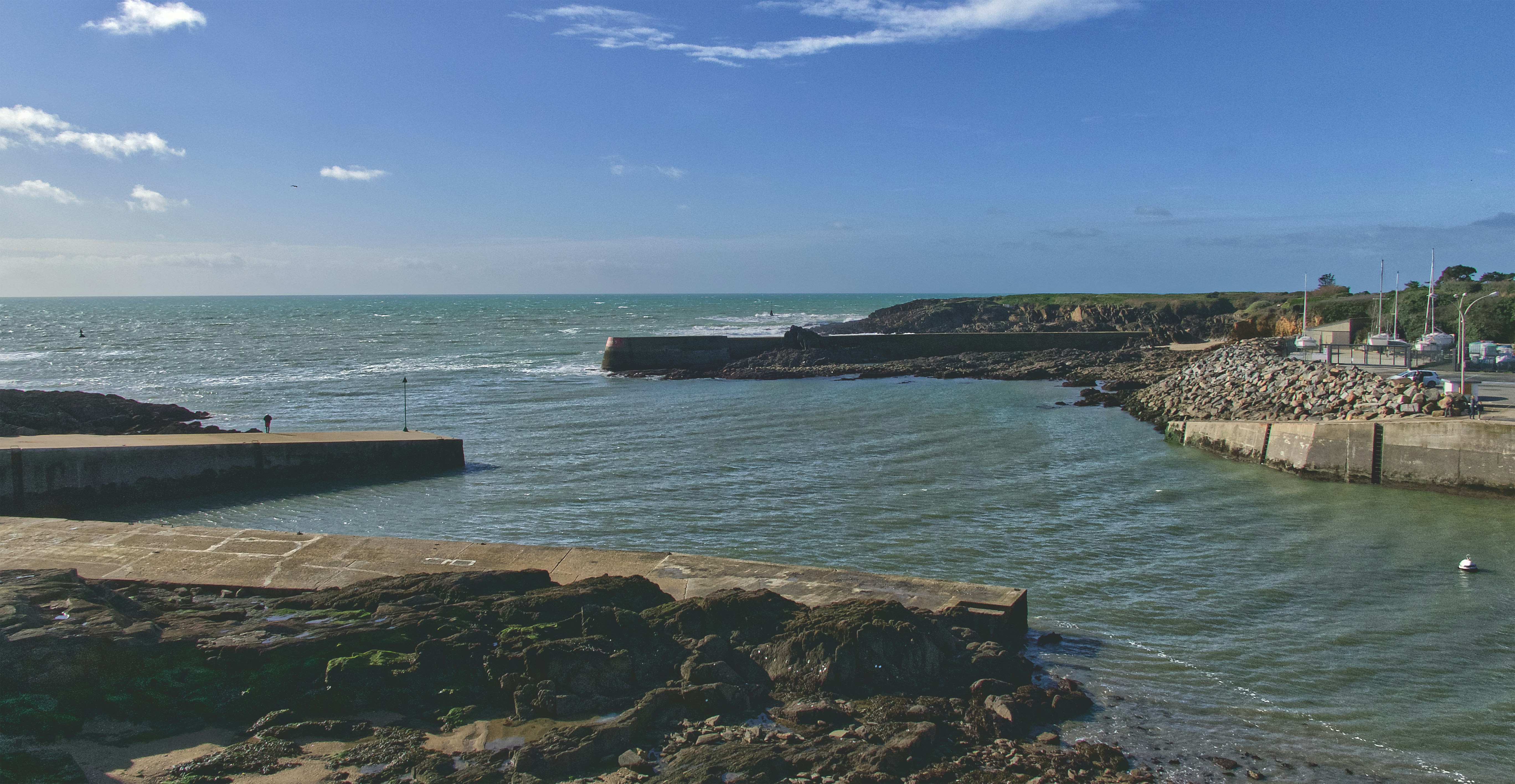 Seaside view of Doëlan harbor with protective jetties and moored boats under a clear blue sky.