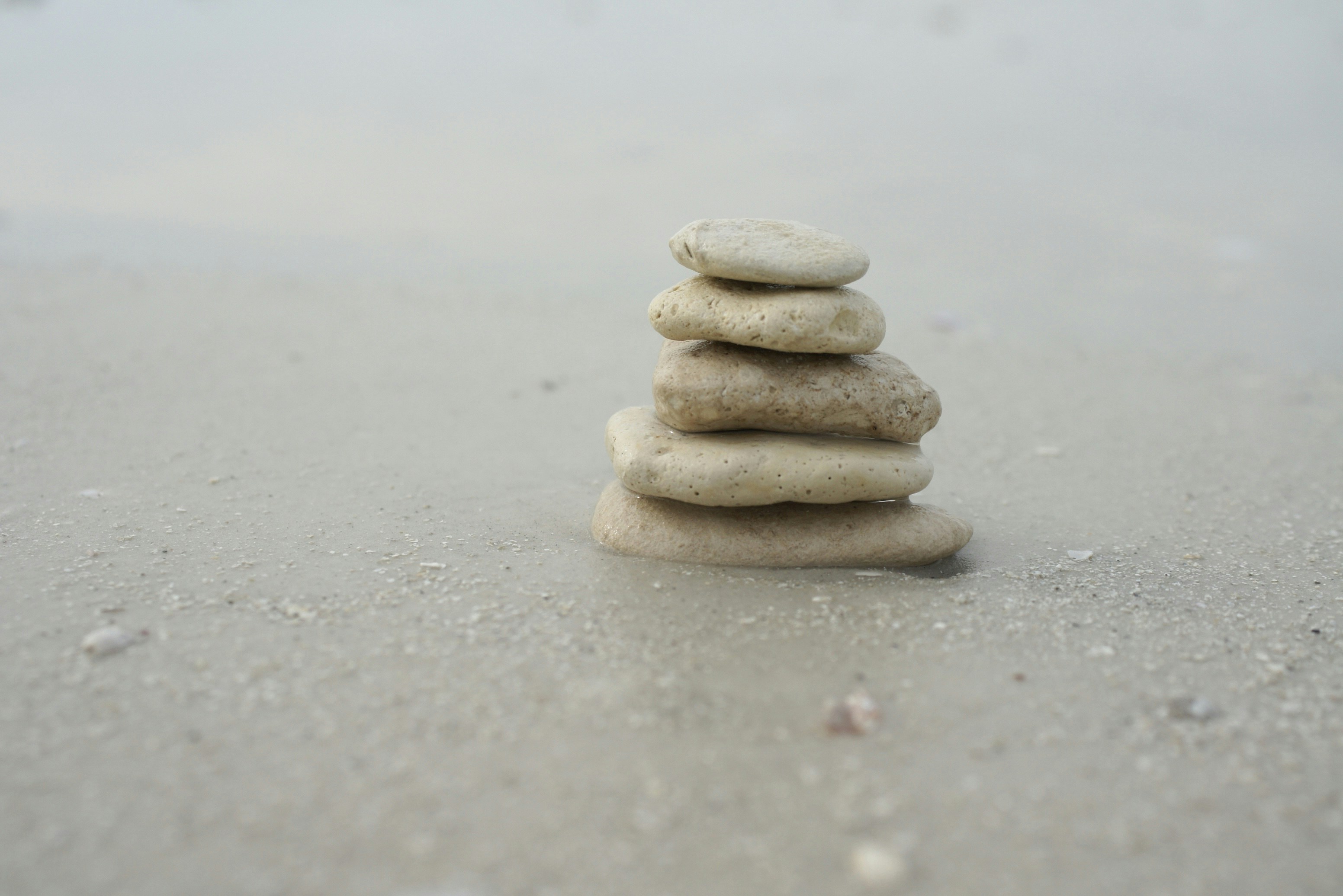 A carefully balanced stack of smooth stones resting on a sandy surface, illustrating the beauty of simplicity and stability.