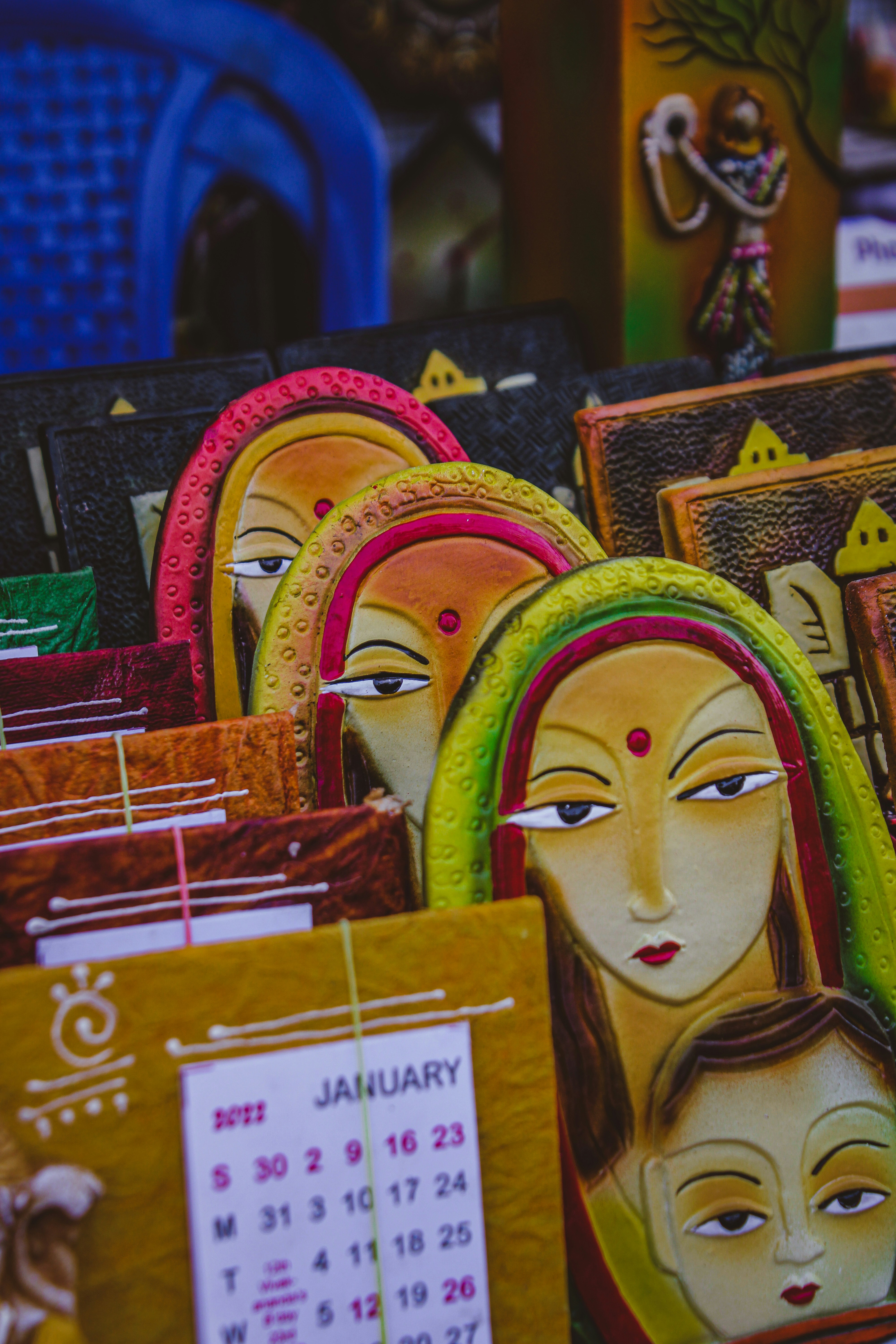 Colorful handcrafted wall hangings featuring stylized faces, showcasing intricate designs and cultural motifs.