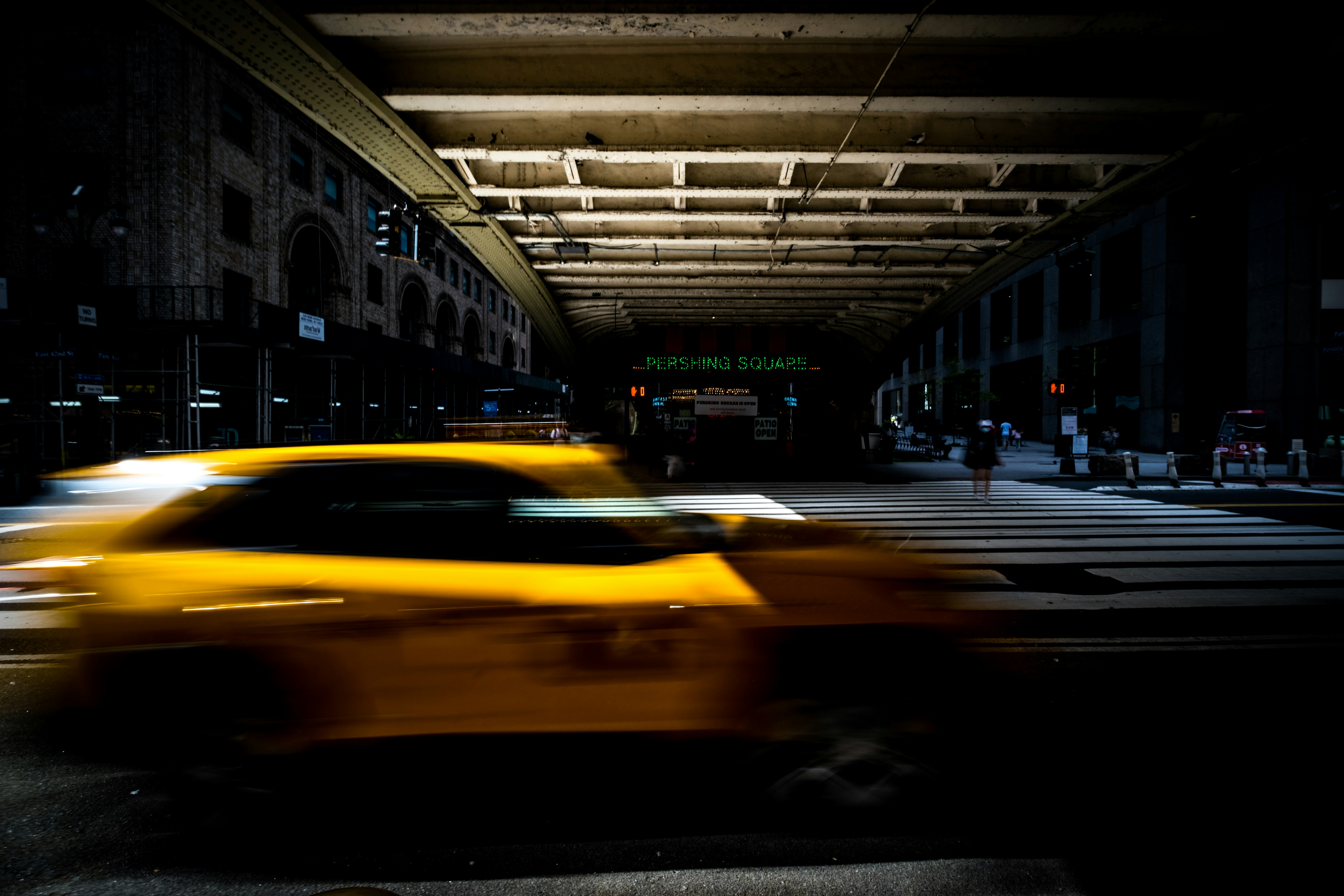 A yellow car driving down a street next to a tall building photo – Free ...