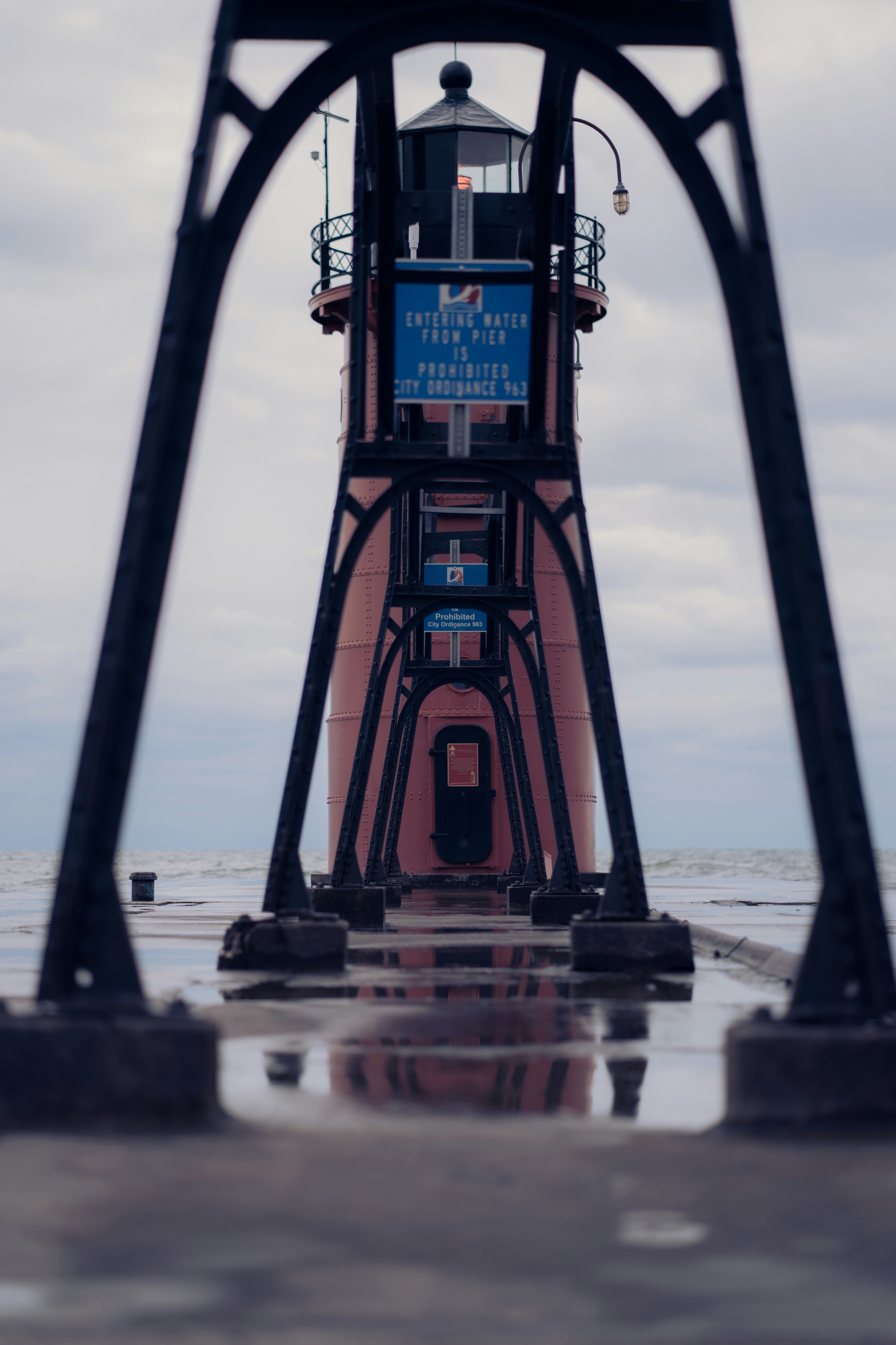 Framed Beacon: Coastal Lighthouse Through the Pier's Iron Arches