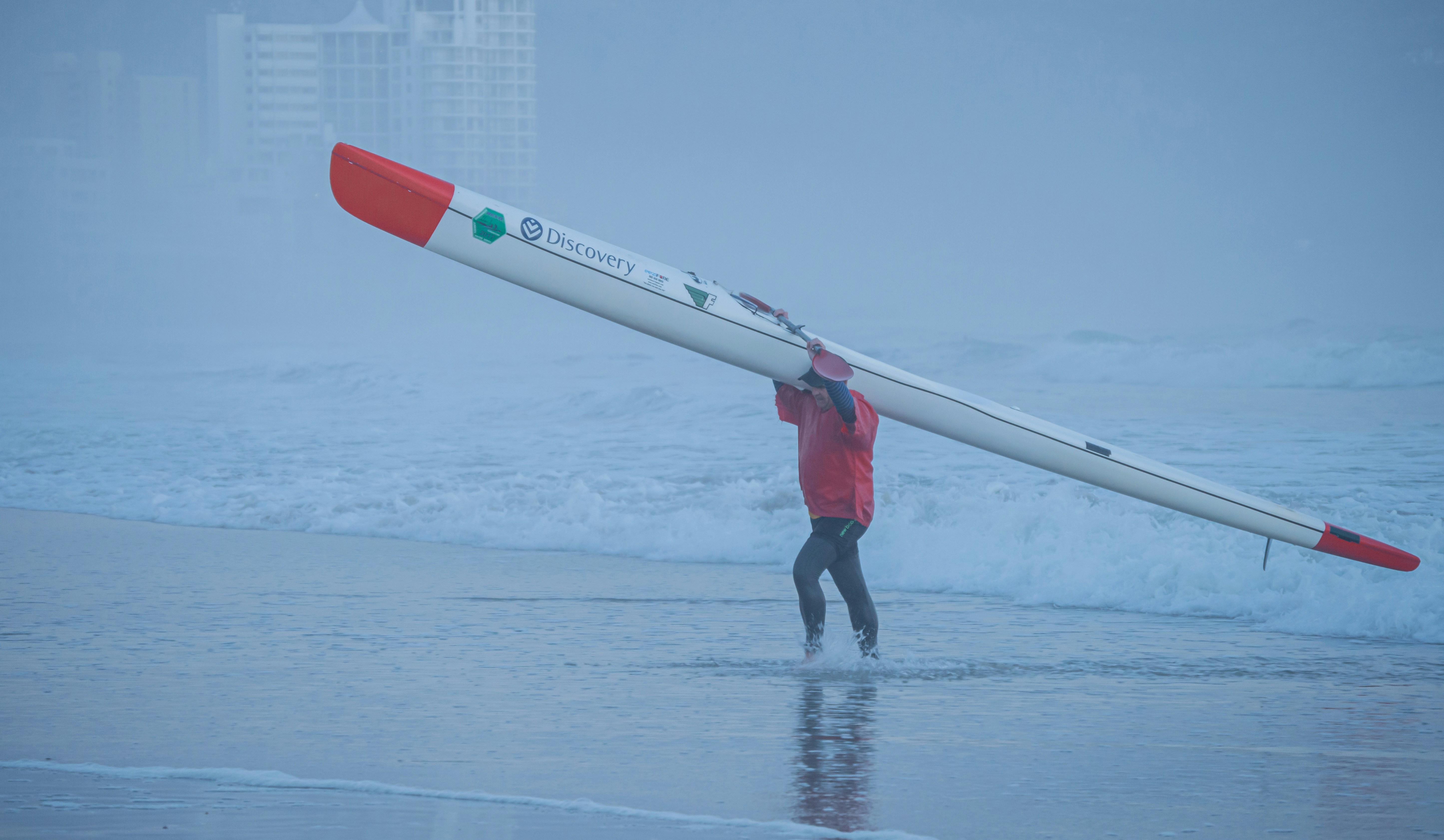 Stormy Light: Surfer Returns with a Red-Rimmed Kite on Shimmering Beach
