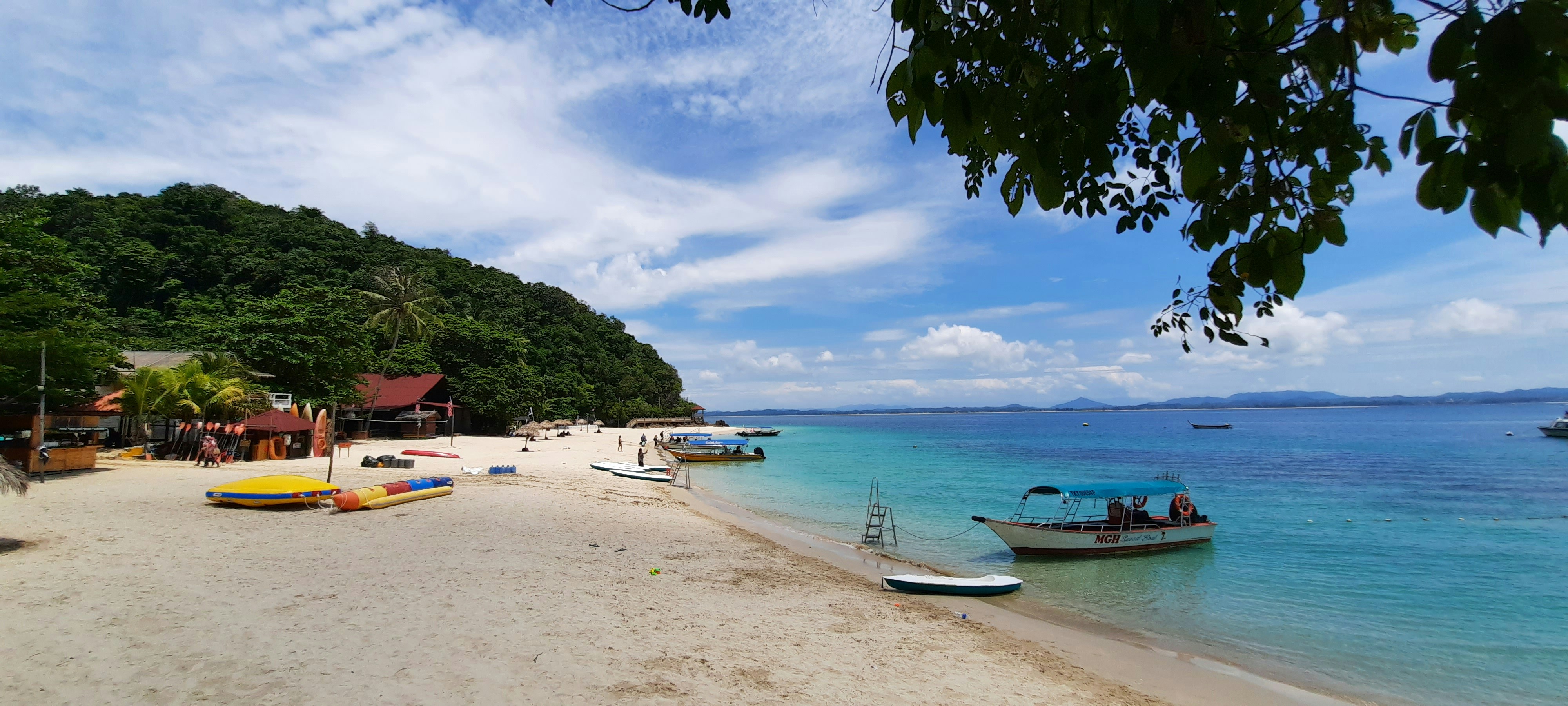 Serene beach scene featuring colorful boats and lush greenery under a bright sky. The calm waters invite relaxation and adventure.