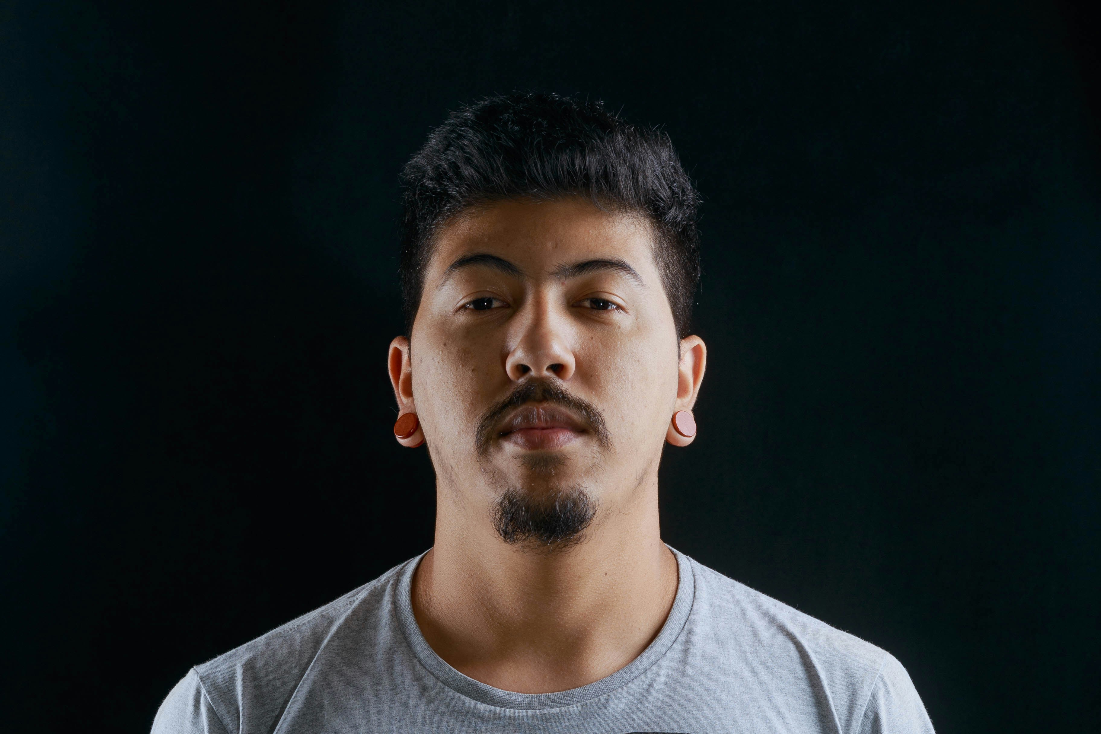 Person in a gray shirt against a dark background, looking directly at the camera.