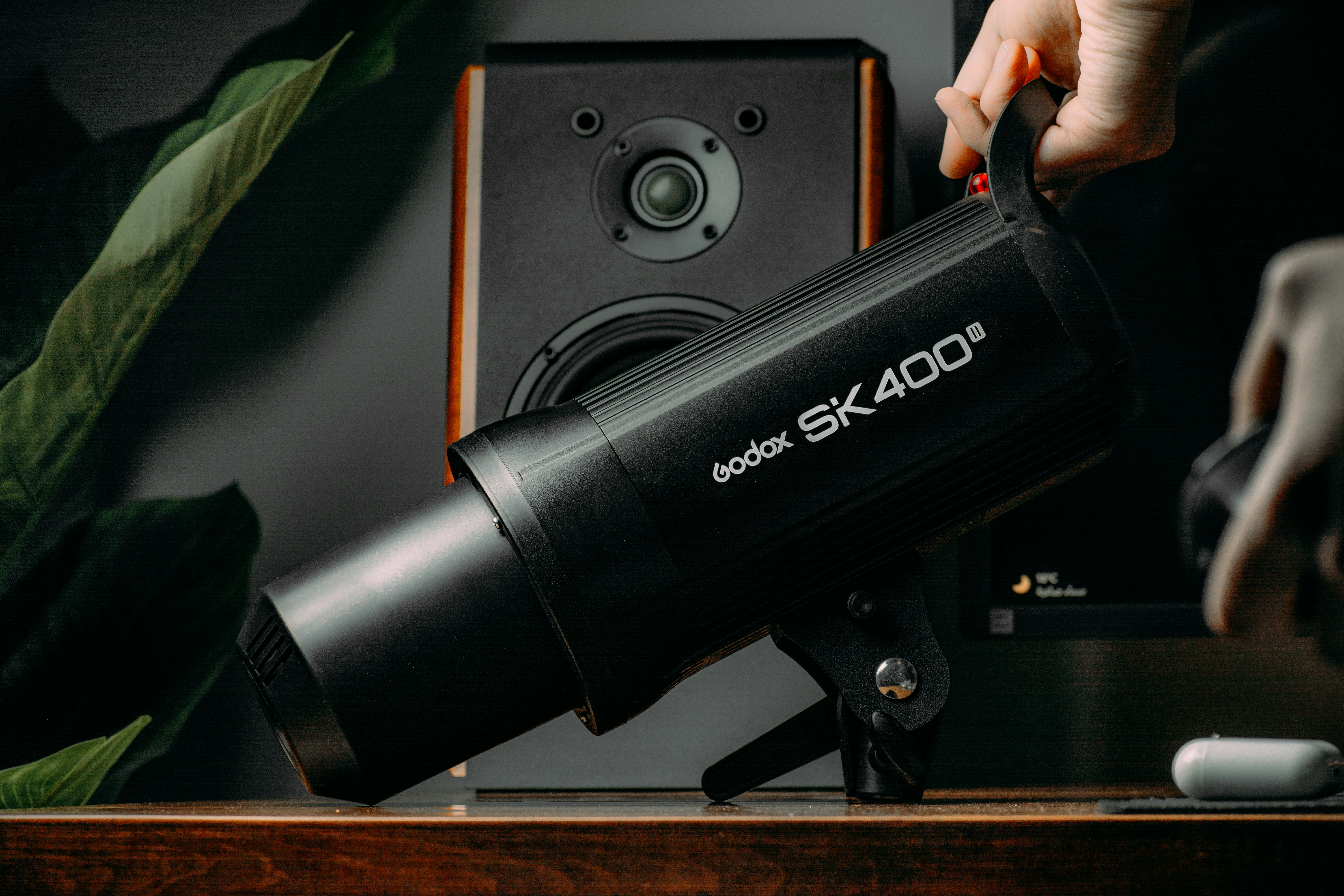 Godox SK400 studio strobe angled on a wooden desk with green leaves in the background.