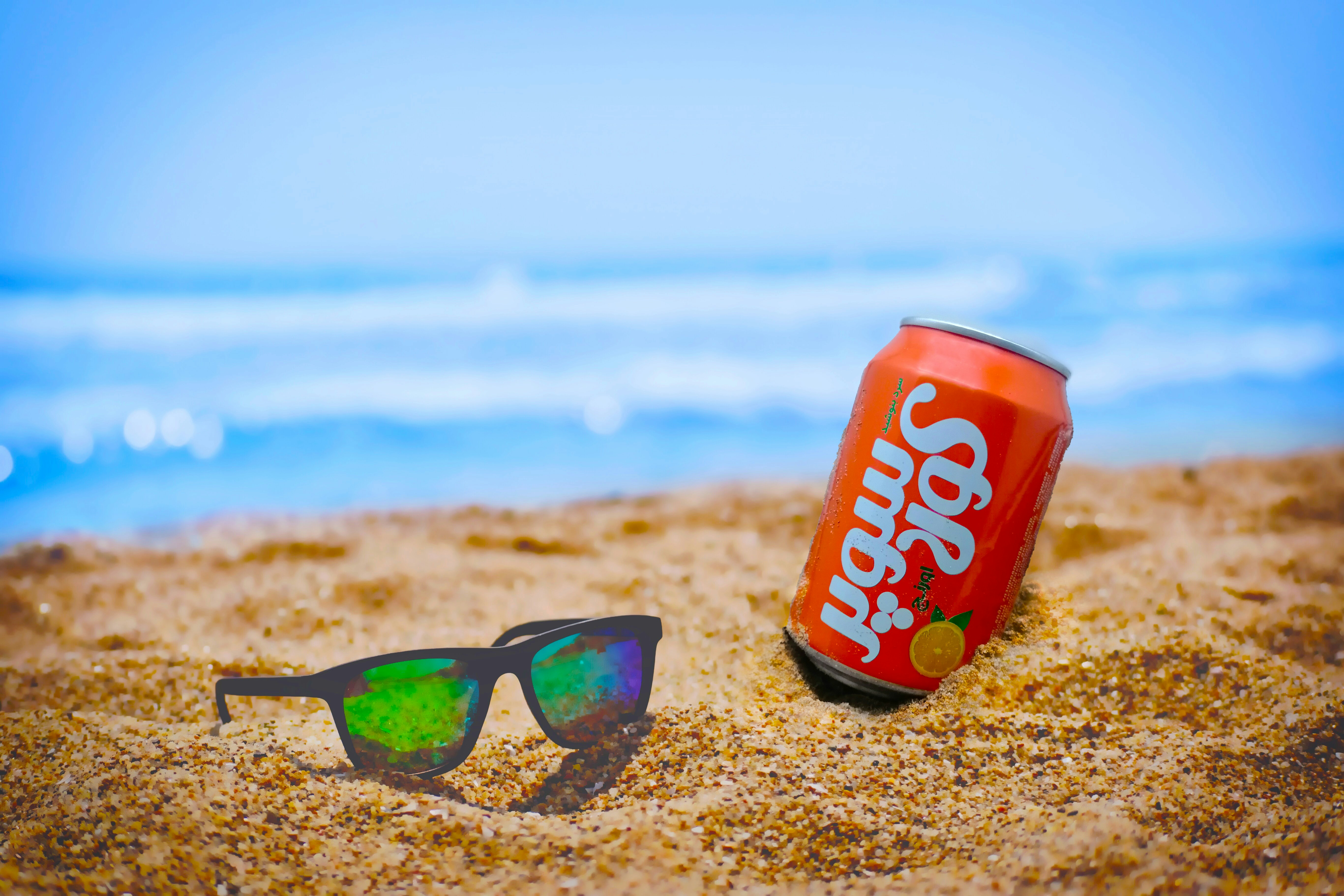 Foto Una lata de refresco y gafas de sol en la playa – Imagen Beber ...