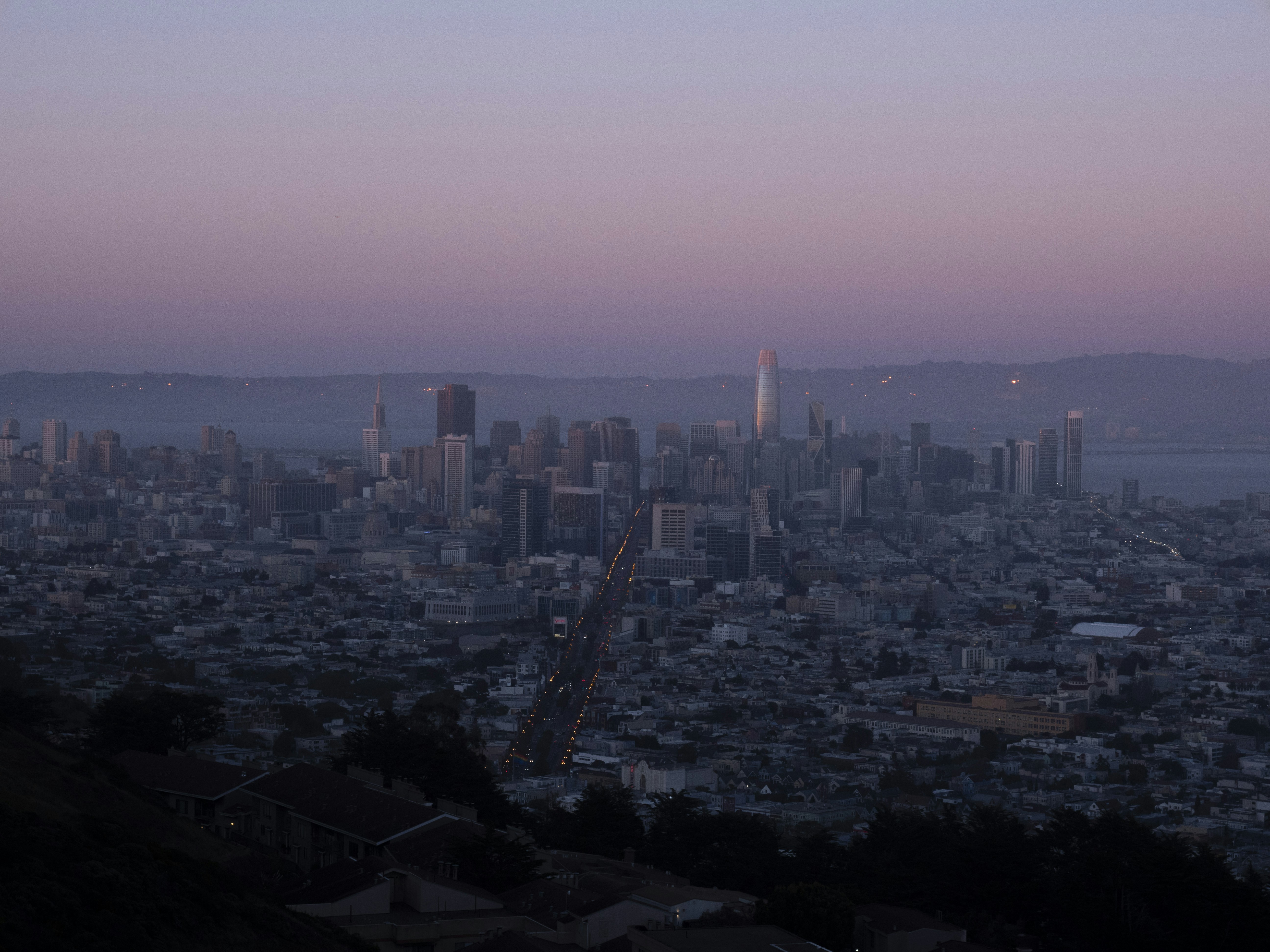 A panoramic view of San Francisco at twilight, showcasing the skyline with prominent buildings and a winding street illuminated by city lights.
