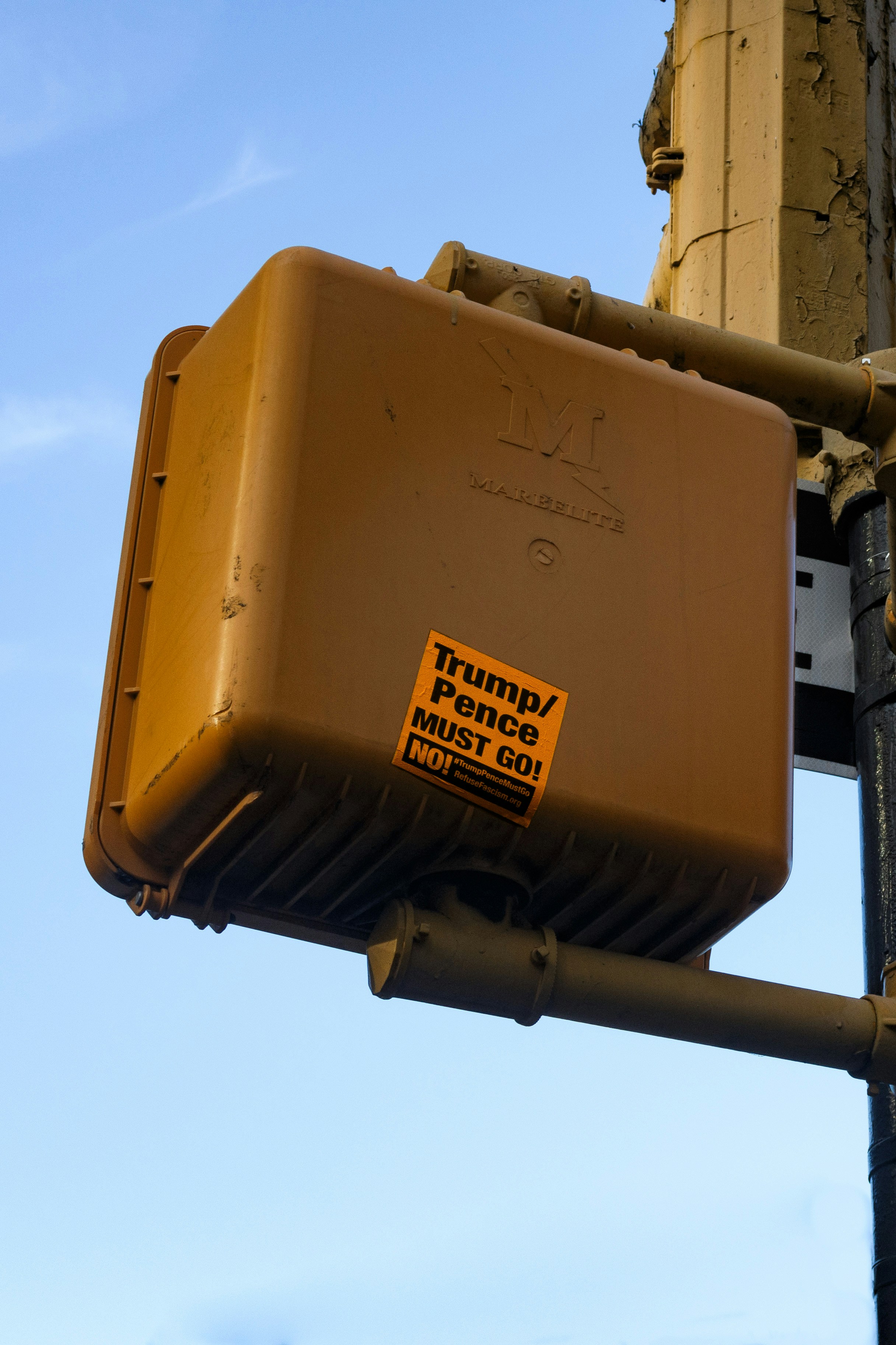 Amber Street Utility Box Under a Clear Blue Sky, Bearing a Trump/Pence MUST GO Sticker