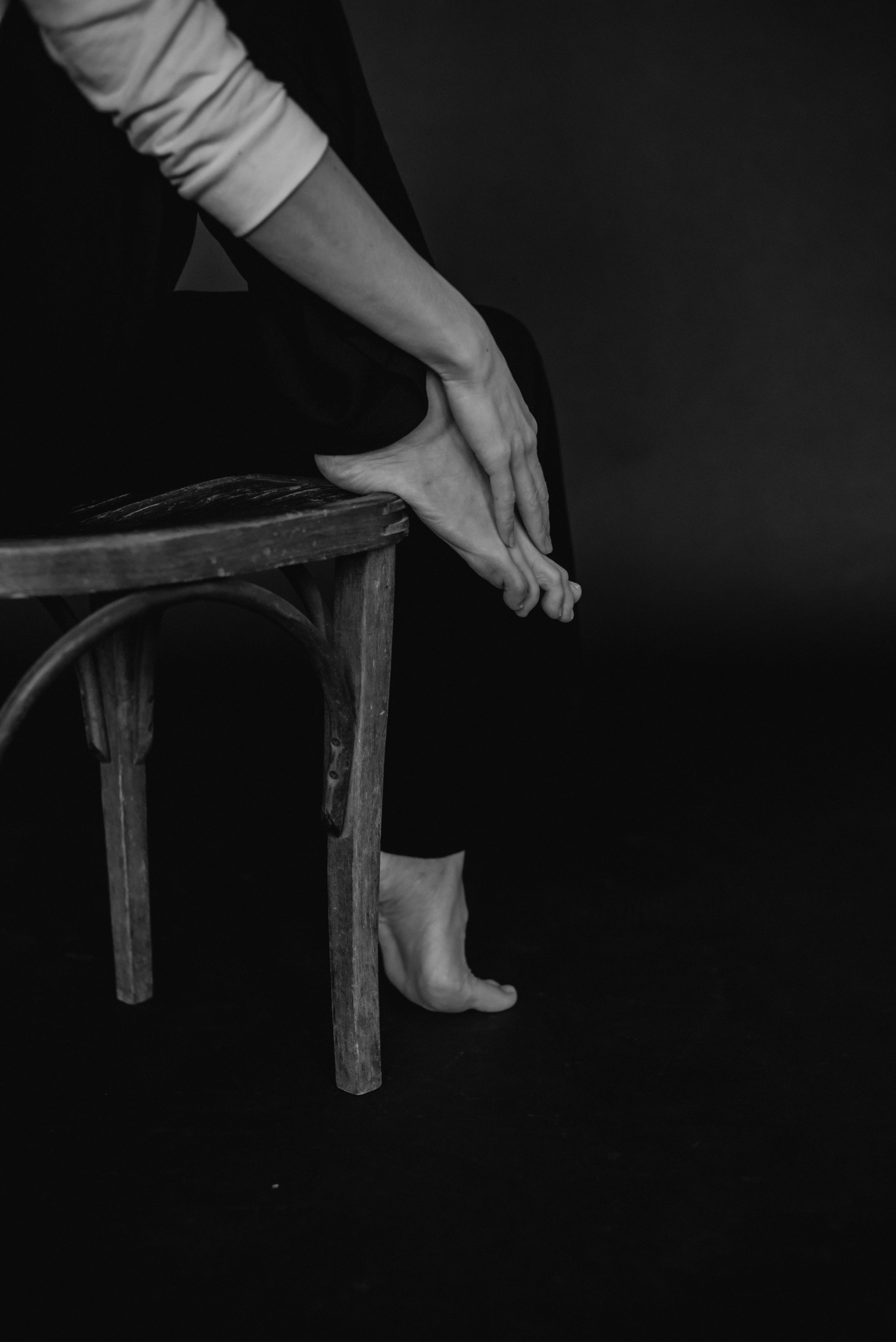 A close-up of a hand gently holding a foot, emphasizing the beauty of human form against a dark backdrop.